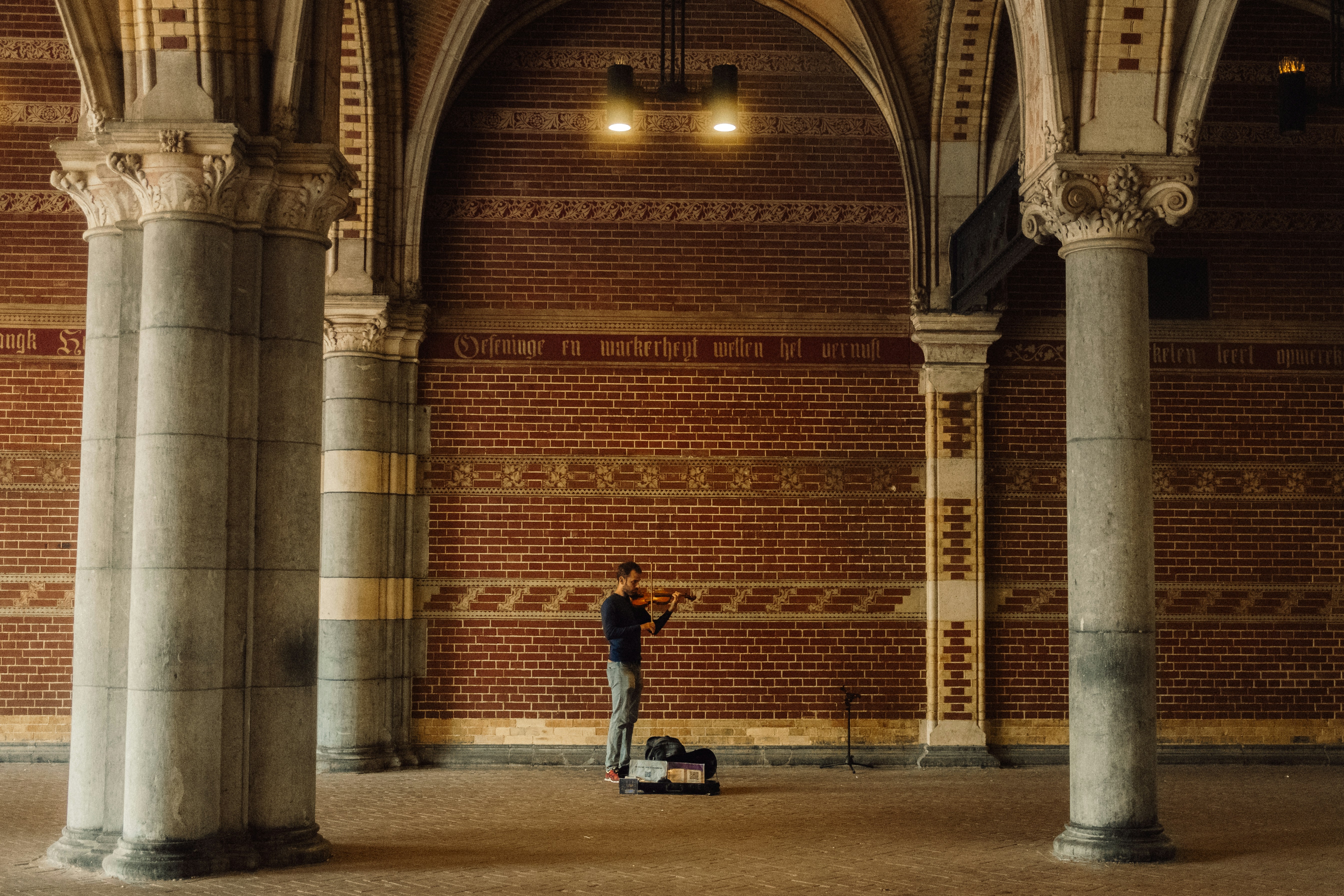 A person playing a violin in a brick archway with stone columns