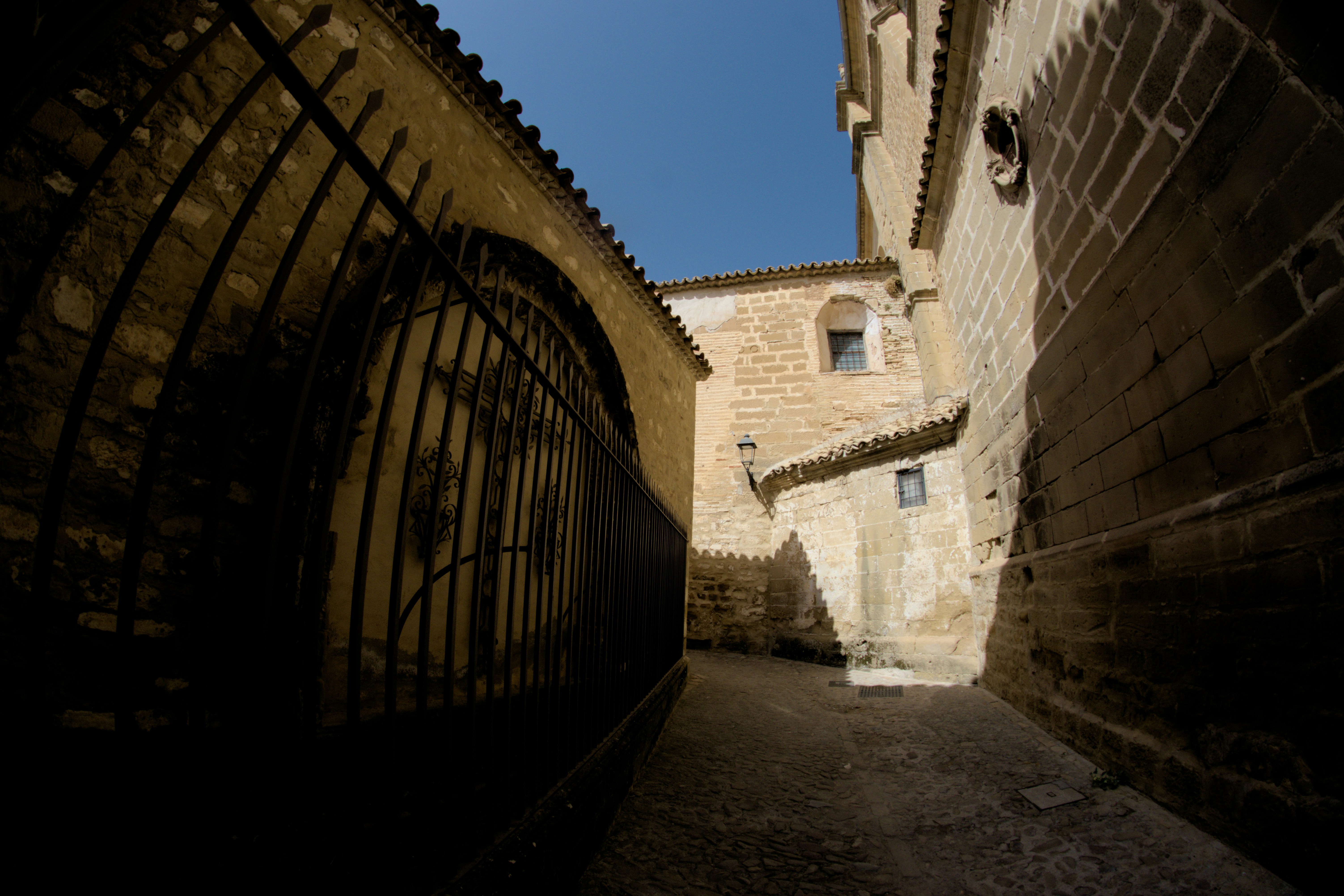 Sunlit Alleyway Convergence: Old Stone Walls and Wrought Iron Gate