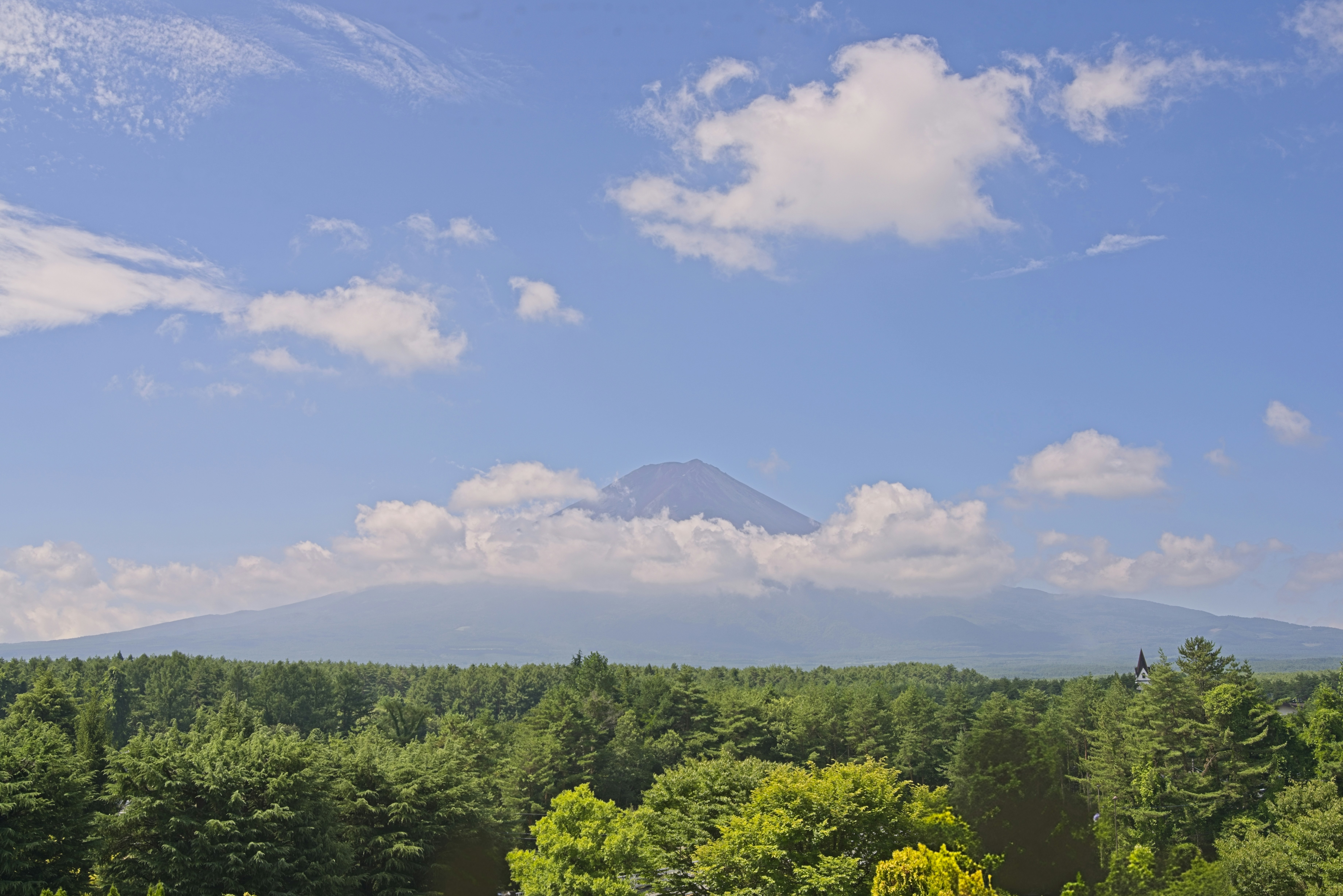 Azure Sky Over Green Crest: Distant Mountain Peeks Through Gentle Clouds