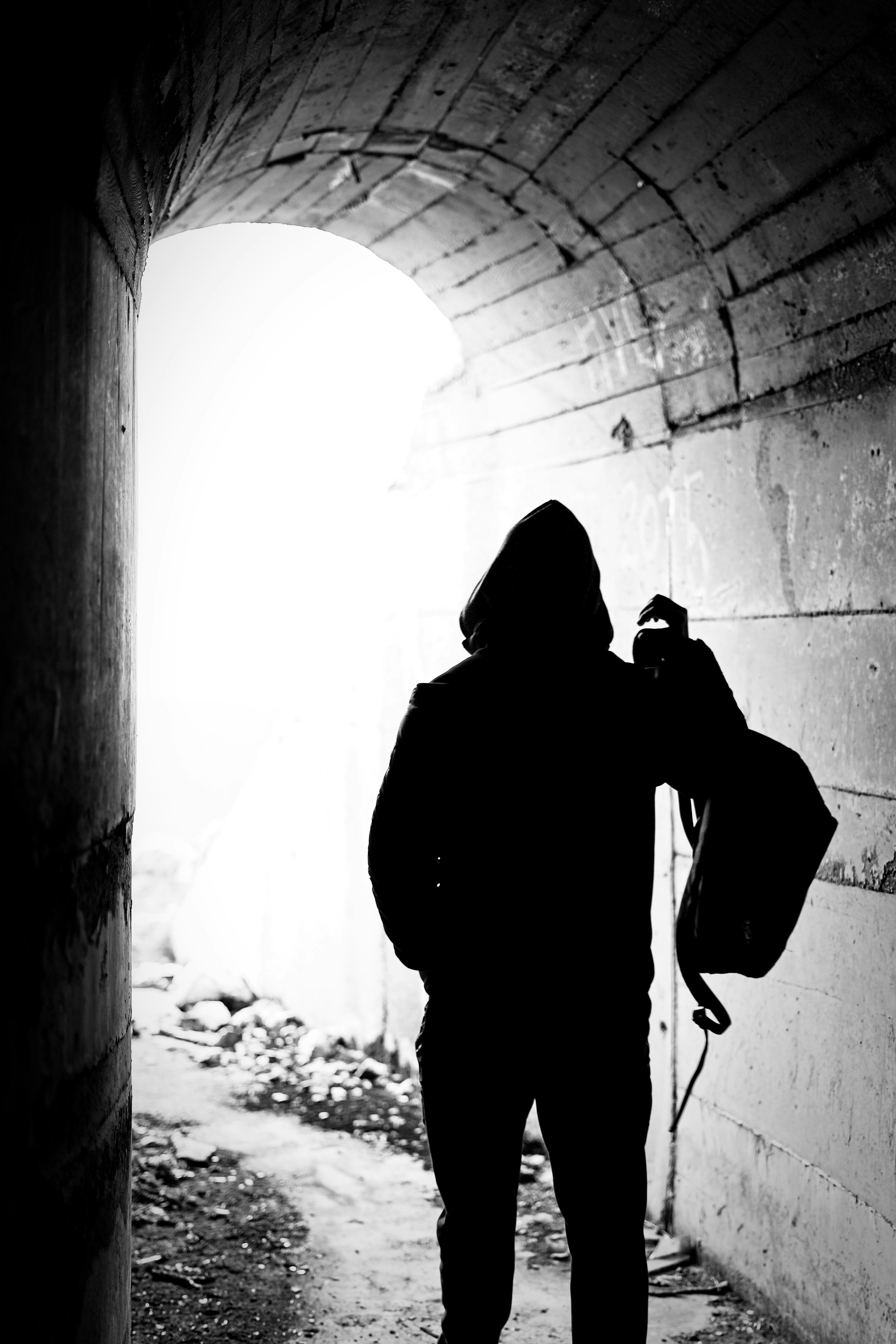 High-contrast silhouette of a photographer with a camera in a tunnel, backlit by bright exit light. Monochrome emphasis on shape and mood.
