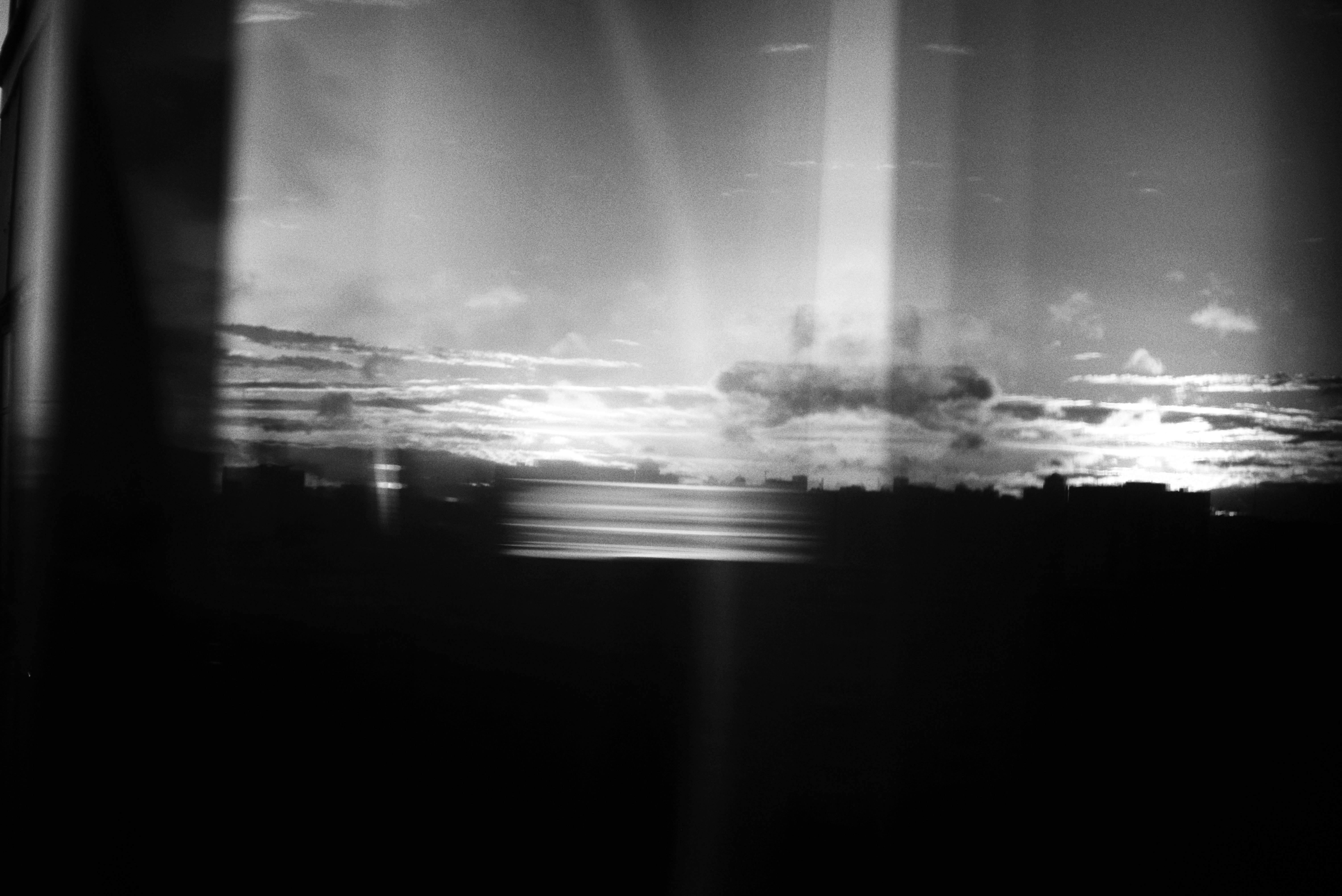 Monochrome seascape with a distant horizon and reflective light along the water, suggesting long exposure and soft movement; a minimal composition with abstract, painterly tones.