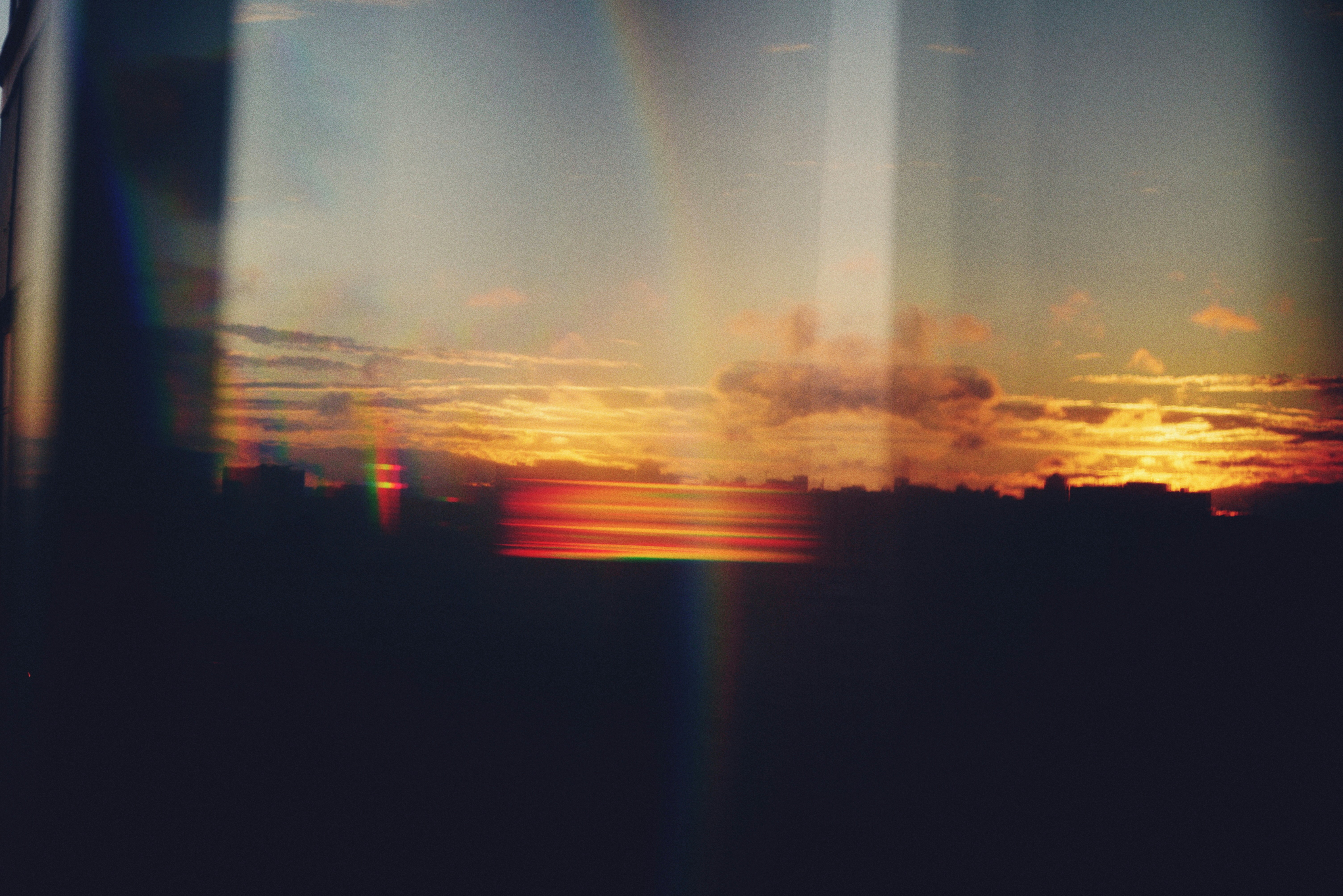 Low-contrast sunset horizon with dark foreground and light streaks across the middle; abstract, likely shot through glass or with motion/flare artifacts.