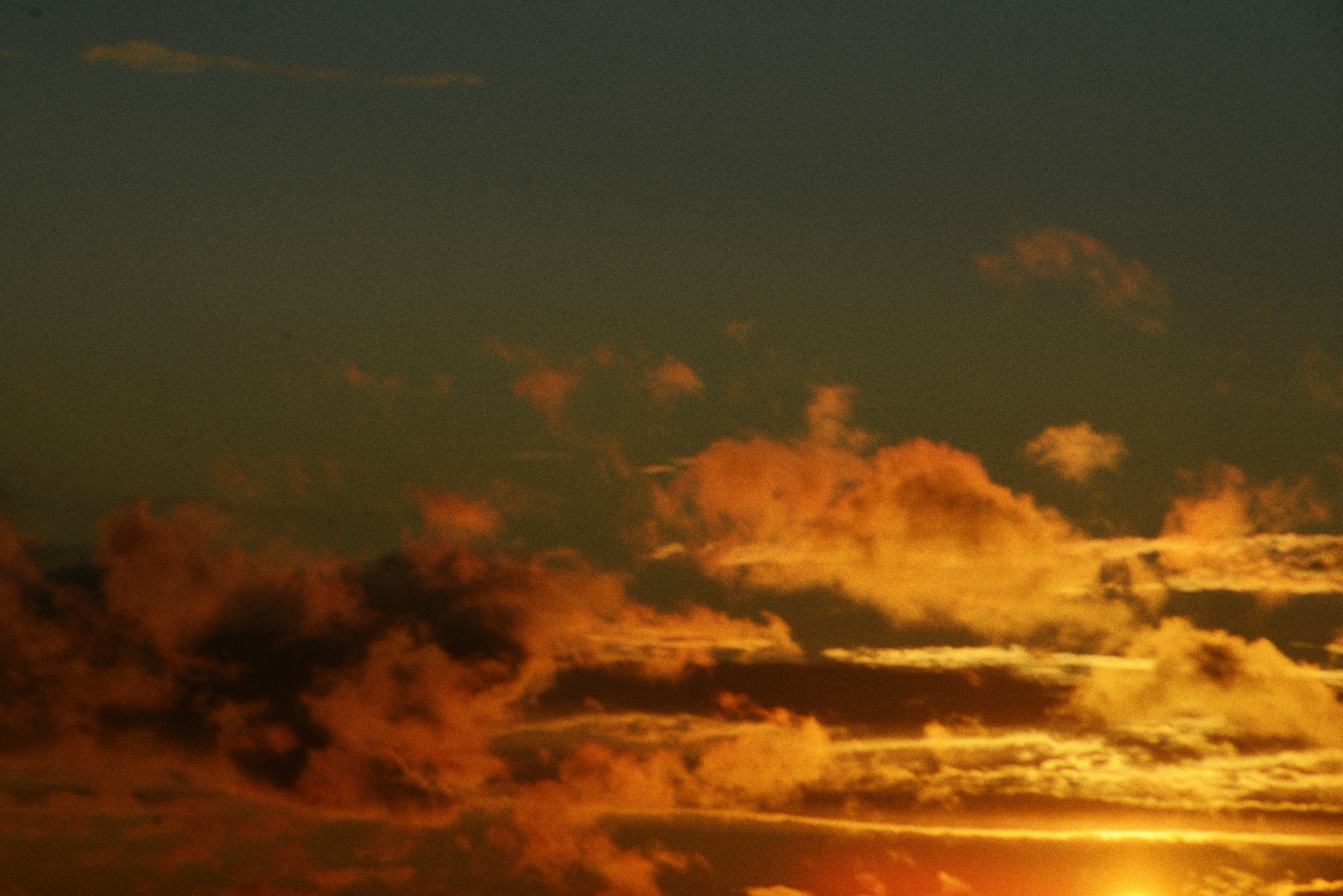 Golden clouds ignite the lower sky as the sun sinks, casting warm hues across the horizon; a serene sunset scene with dramatic cloud textures.