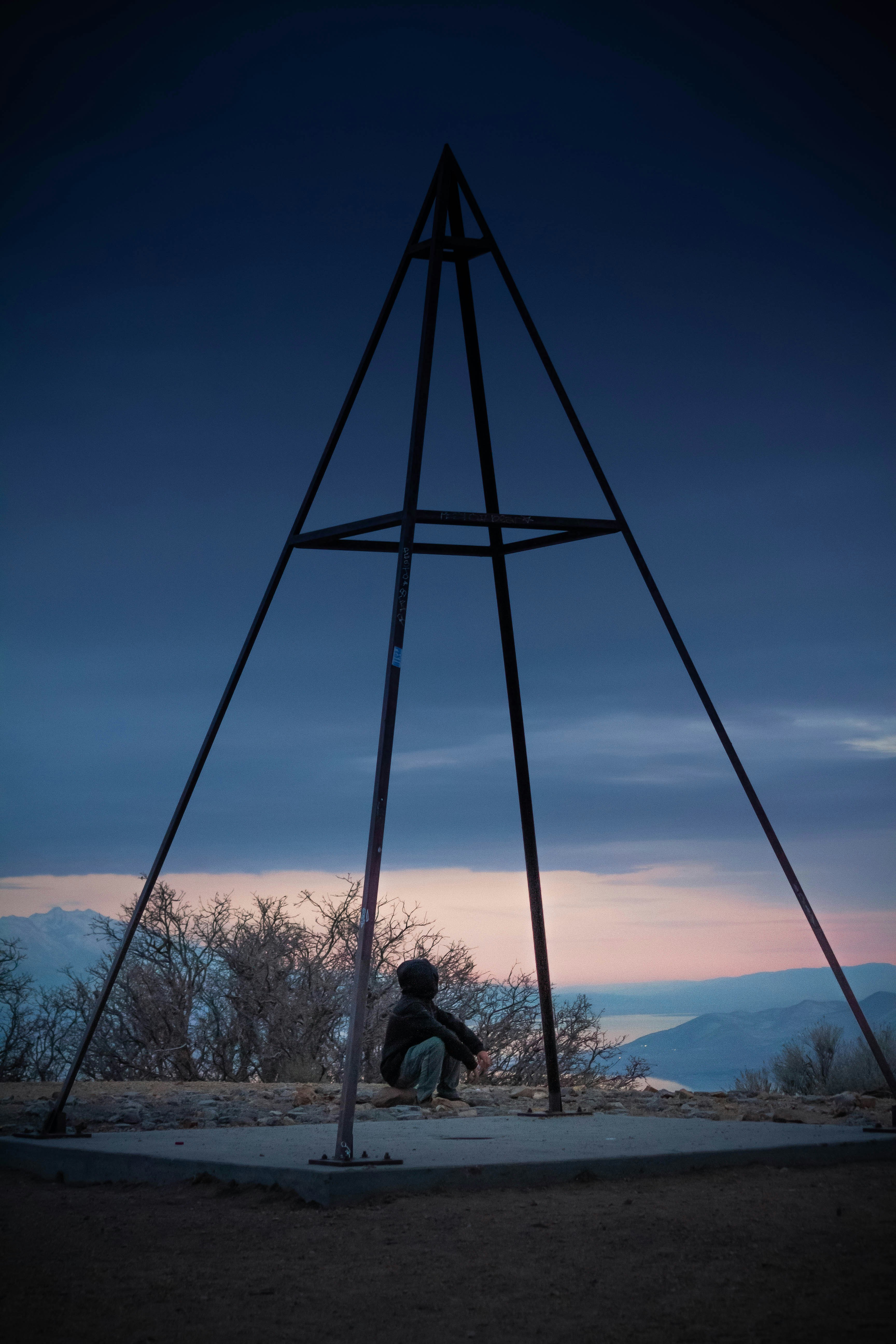 Solitary figure beneath a skeletal monument at twilight