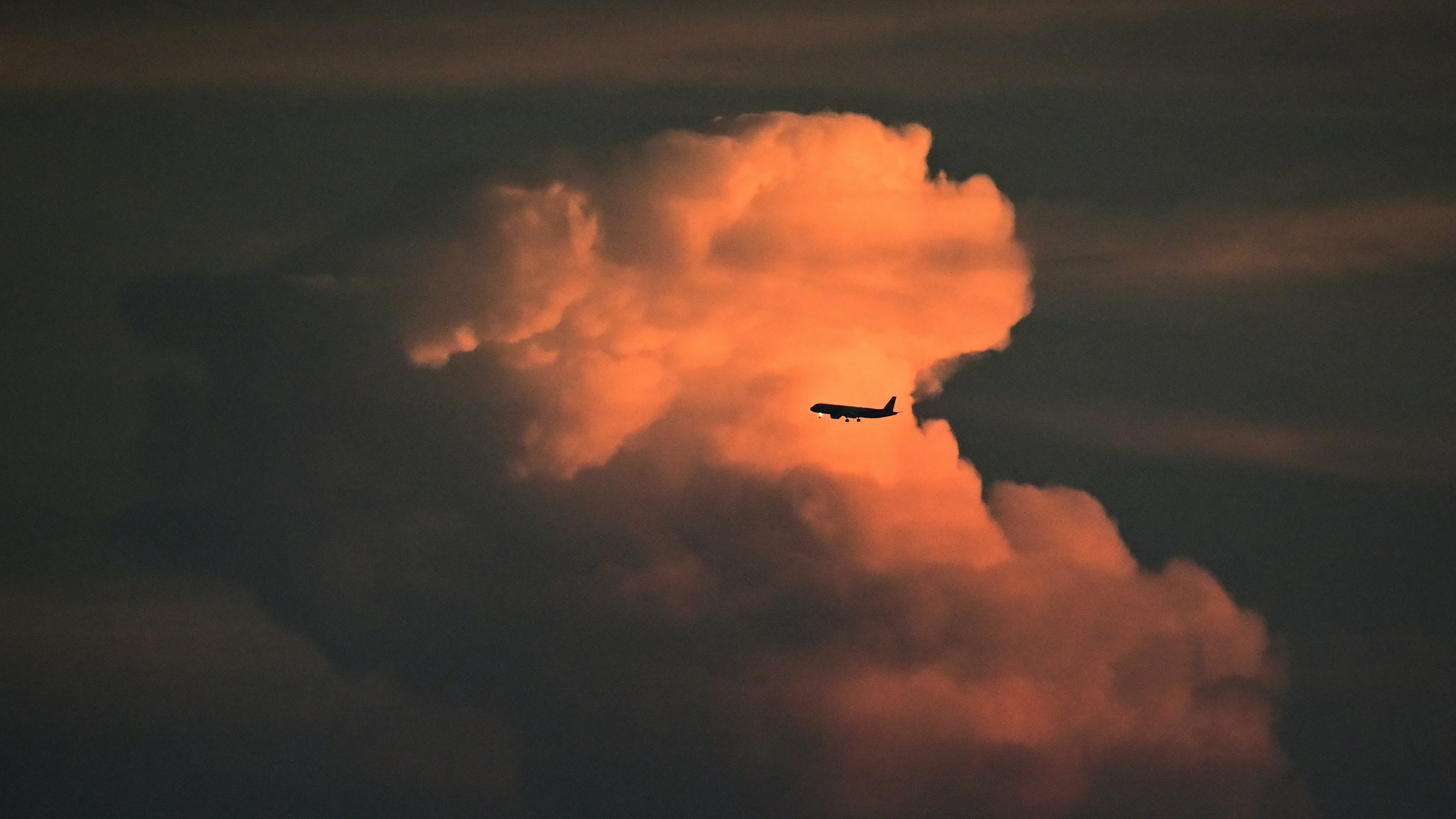 Silhouette in the Ember: A lone jet against a glowing cumulonimbus