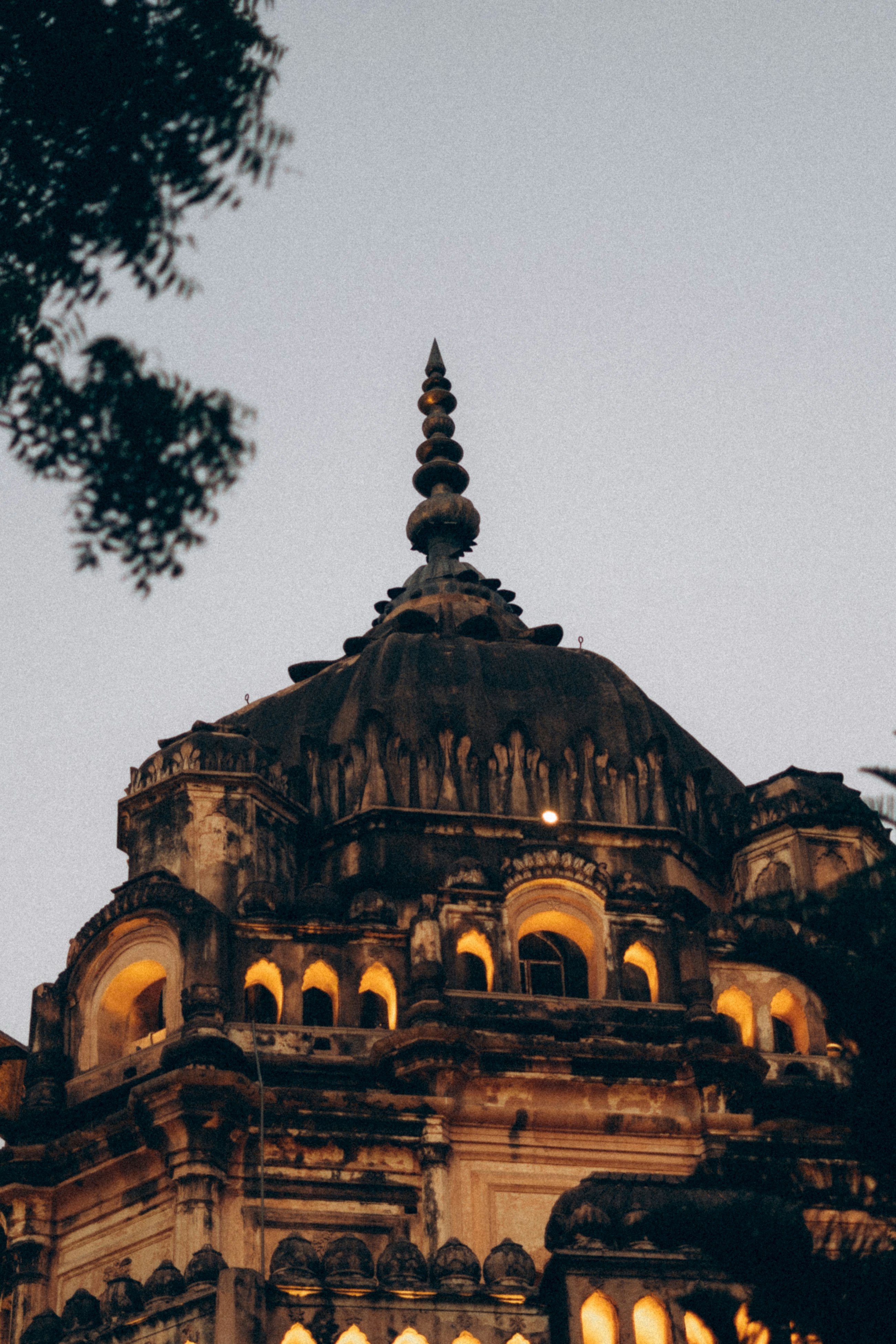 Ornate temple facade bathed in warm lights against a dusky sky, revealing intricate arches and a tiered spire.