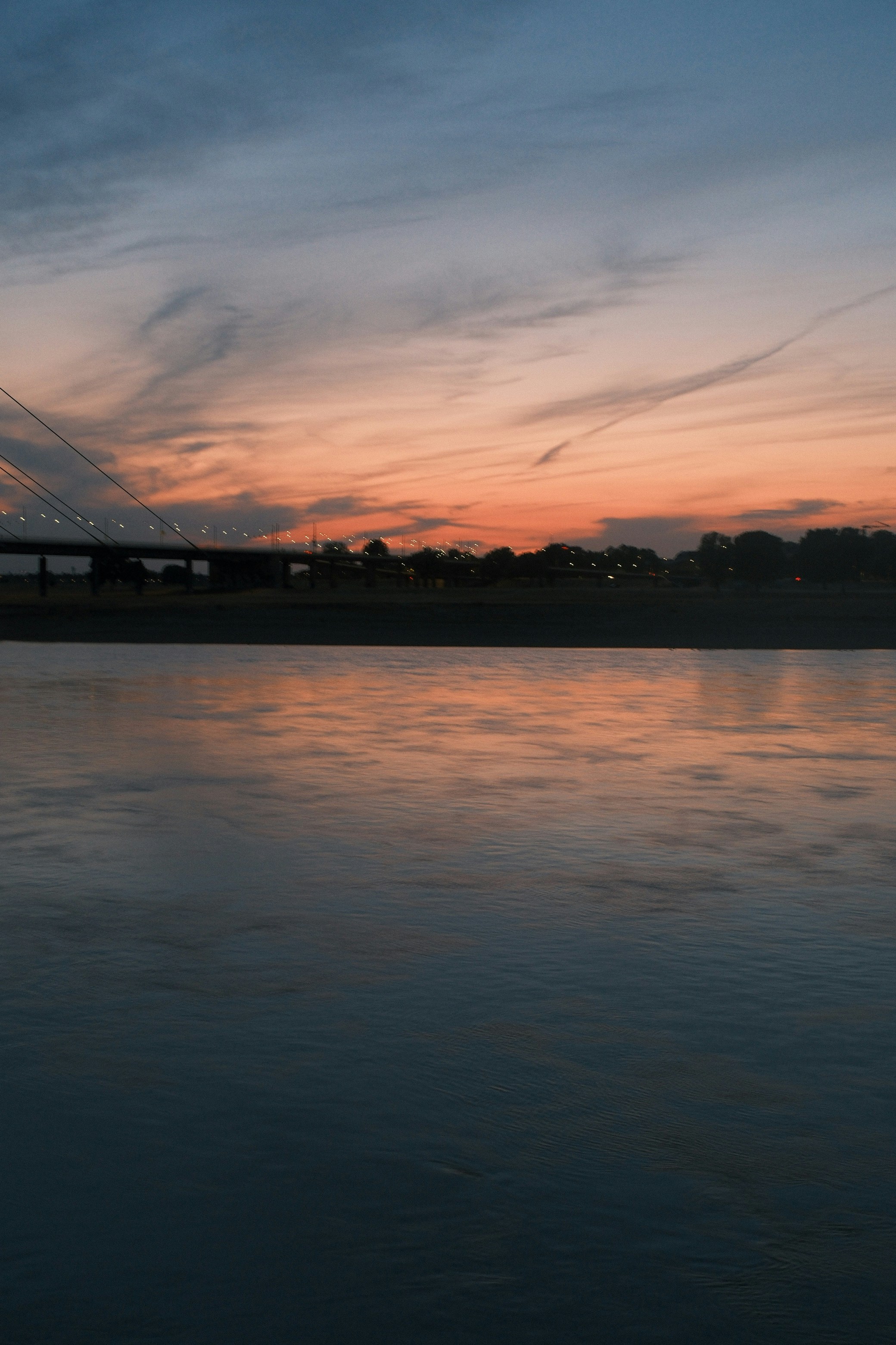 A Quiet Riverside Sunset Beneath a Lighted Bridge