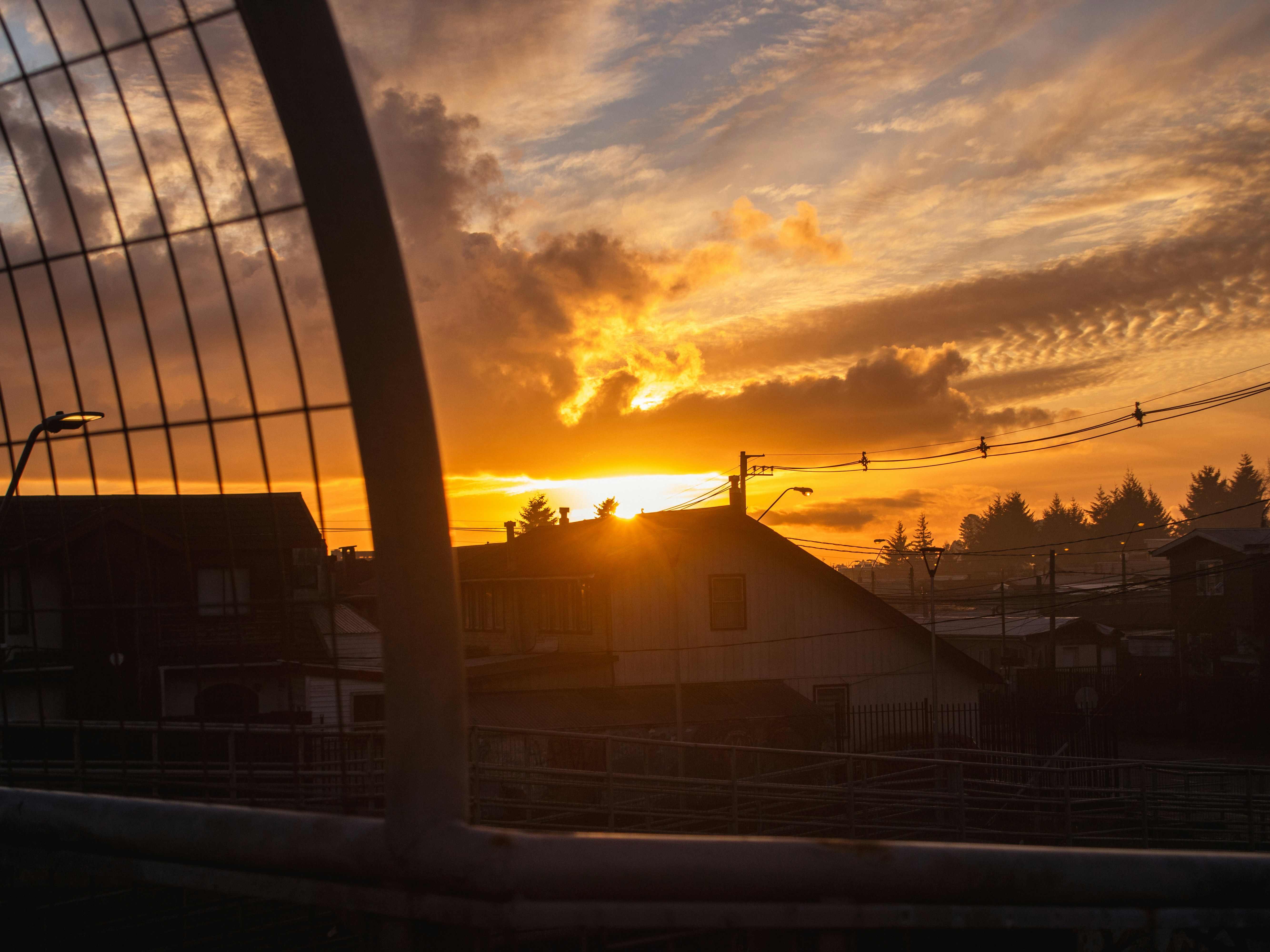 Low-contrast city silhouette bathed in warm sunset light, with a curved bridge railing and power lines framing the scene.