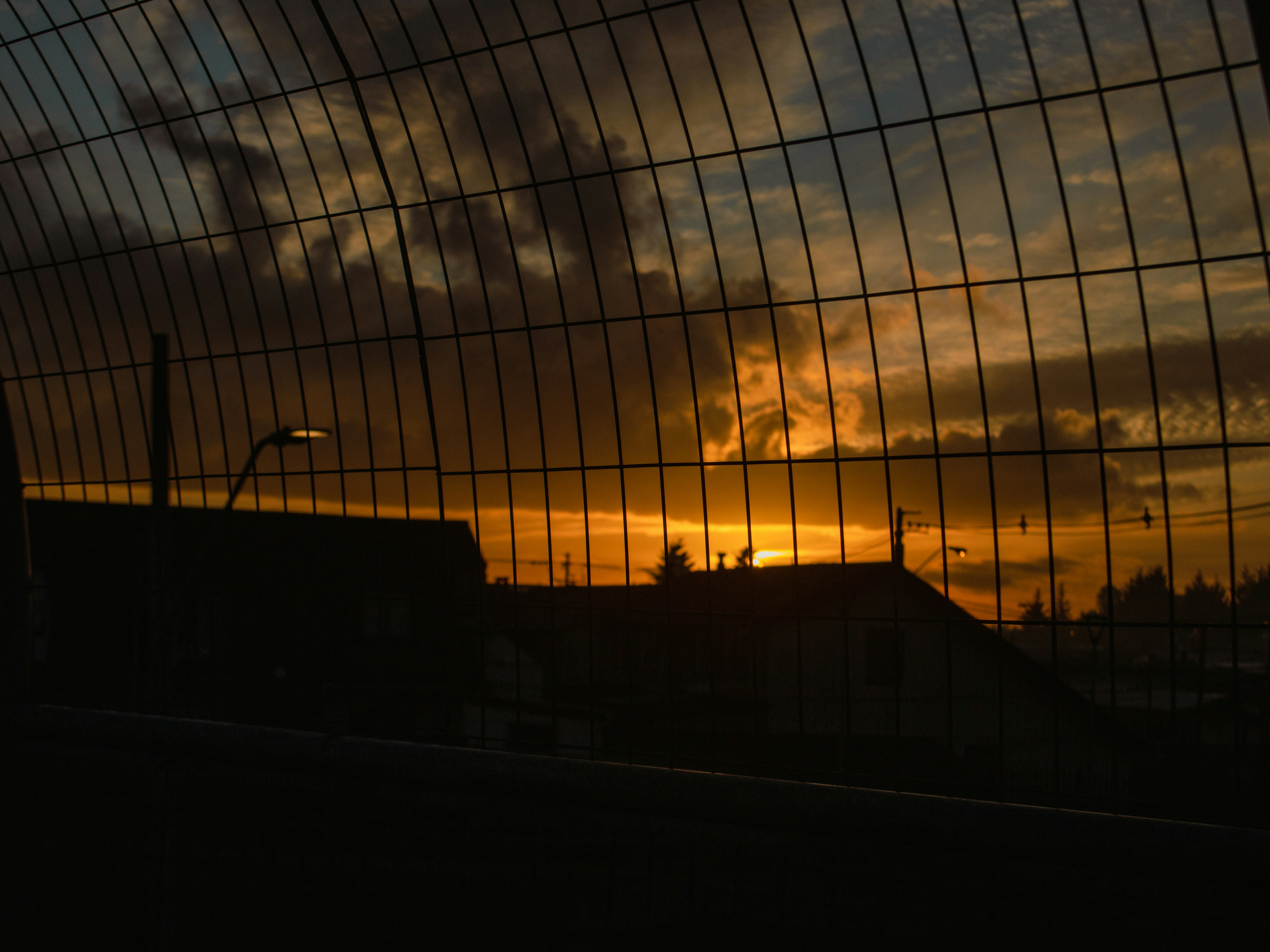 Sunset Dunes Behind a Grid: Silhouetted Fence Over an Industrial Skyline