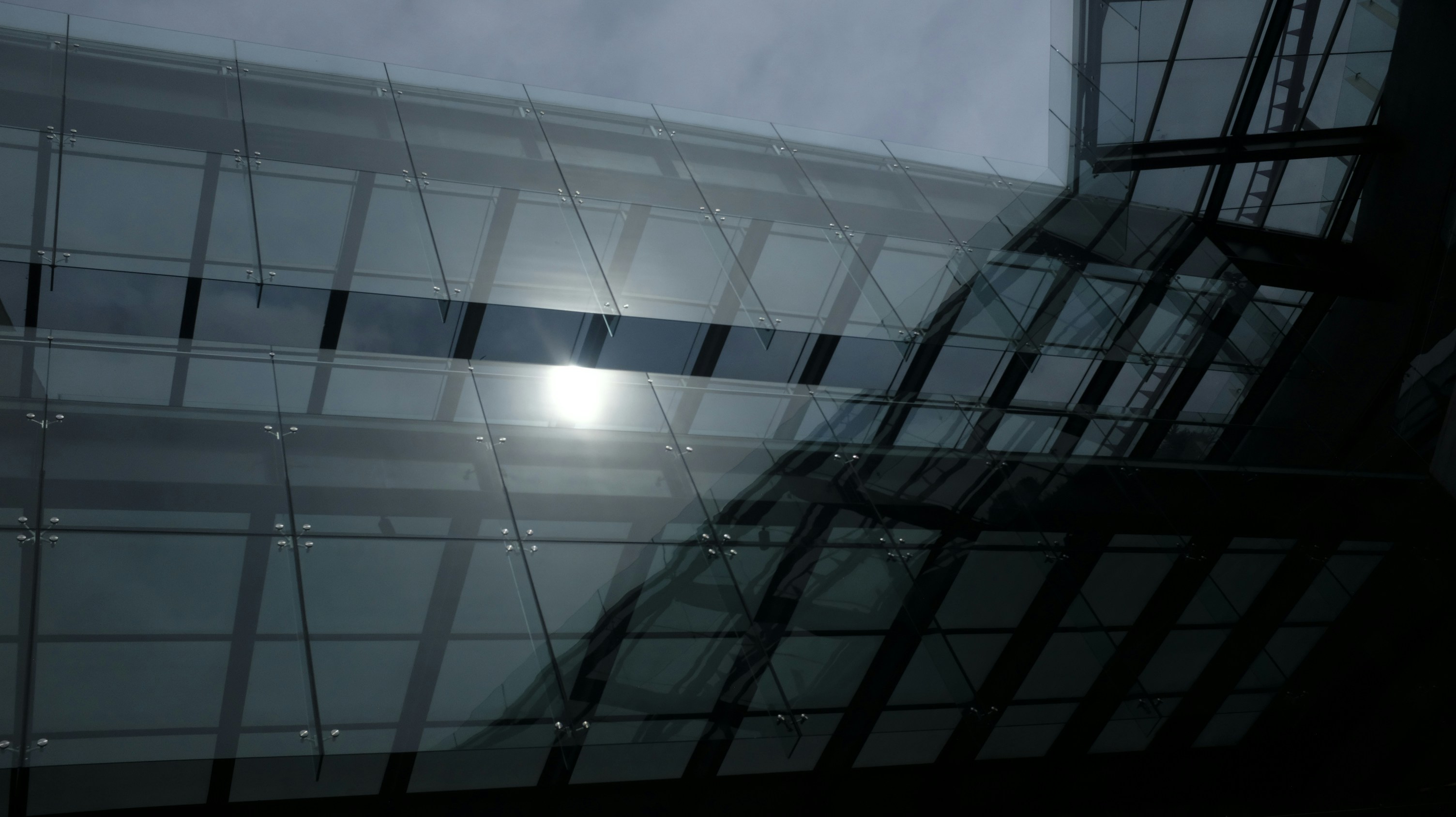 Sunlit Glass Ribbon: Architectural Reflections Across Faceted Facade