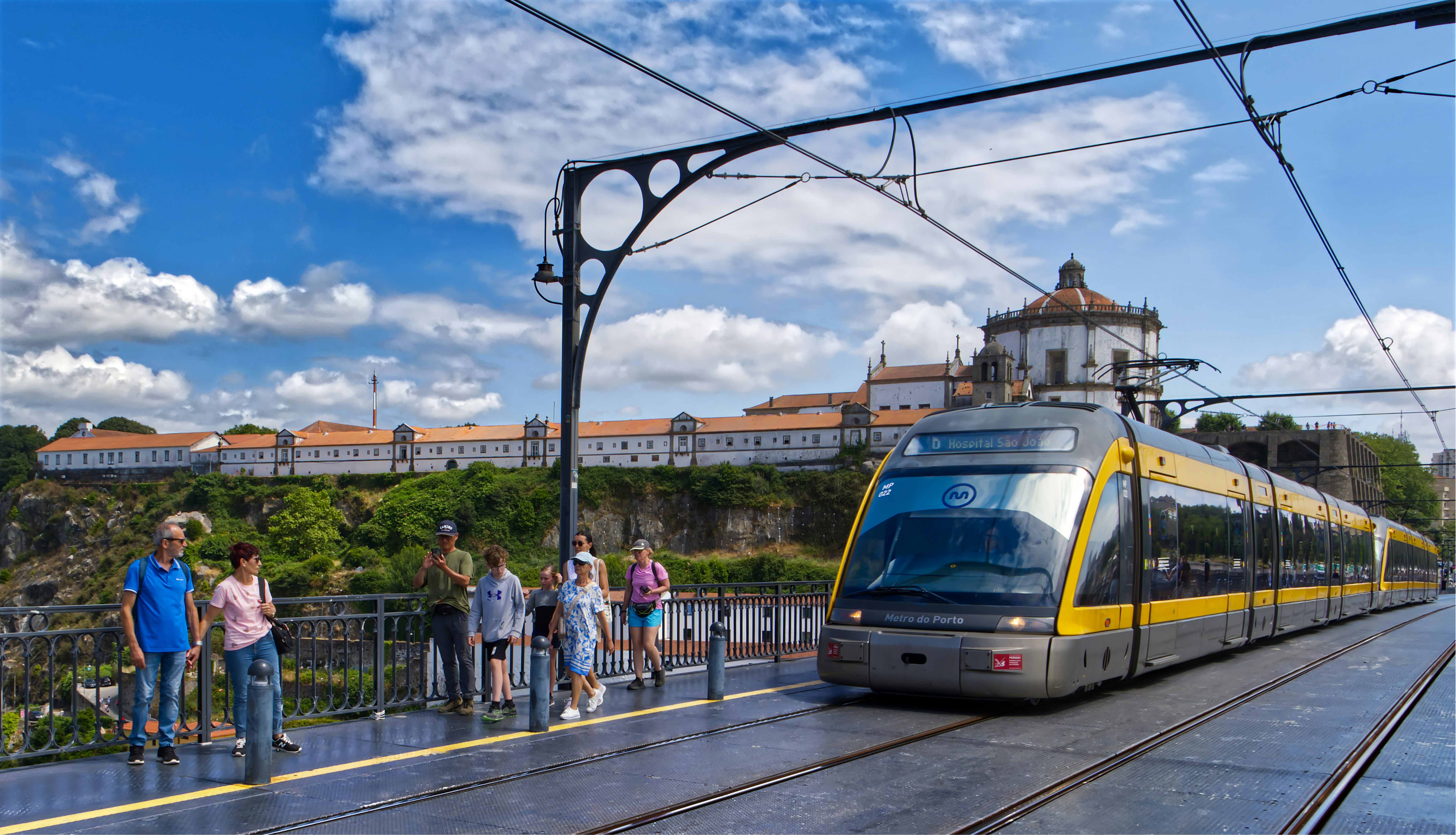 On the Bridge: A City Tram Glides Past a Group by the River