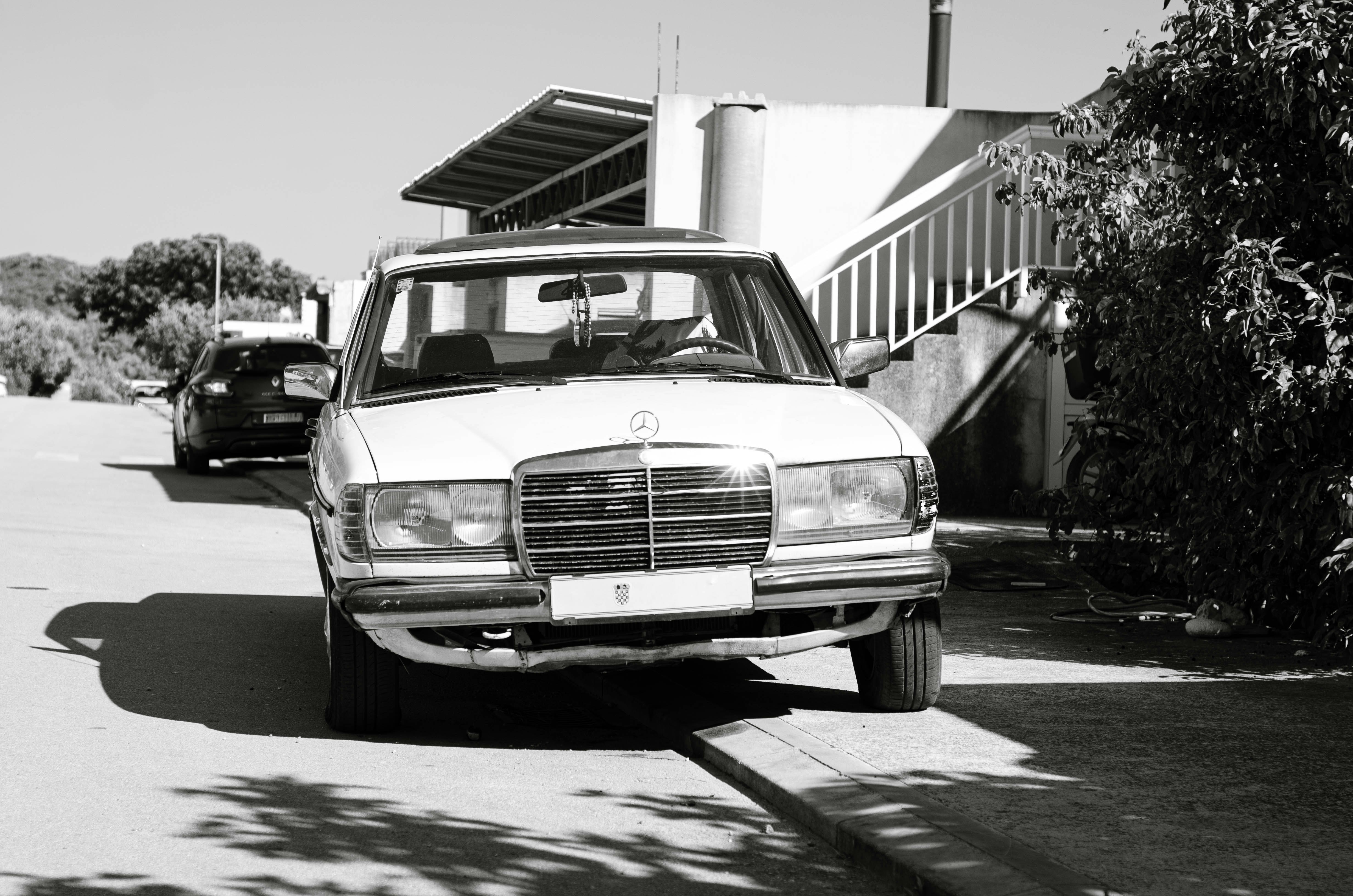 A classic vintage Mercedes sedan parked on a curb, shot in black and white with strong side shadows and a blocky façade.