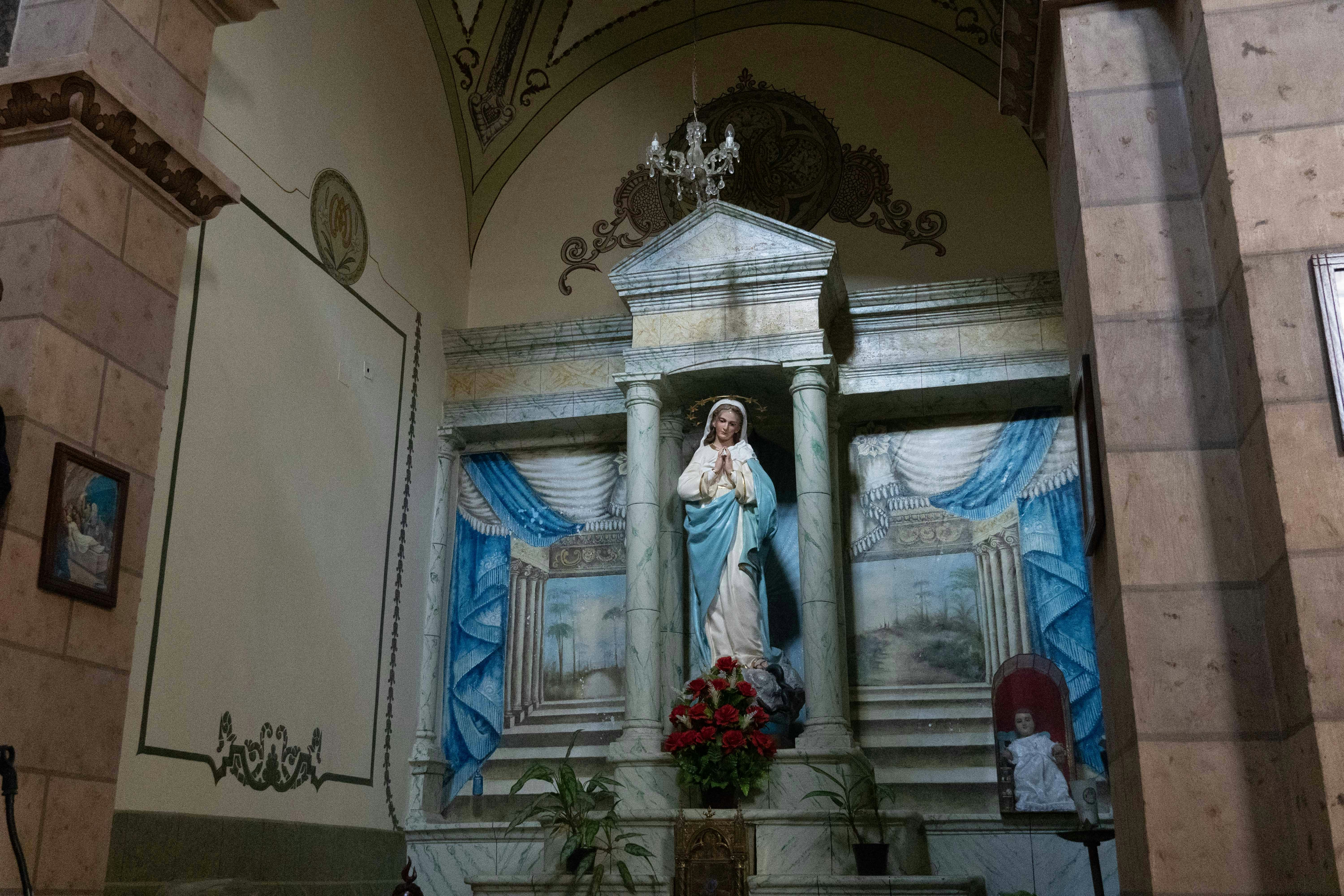 Statue of the Virgin Mary within a church niche framed by draped blue curtains