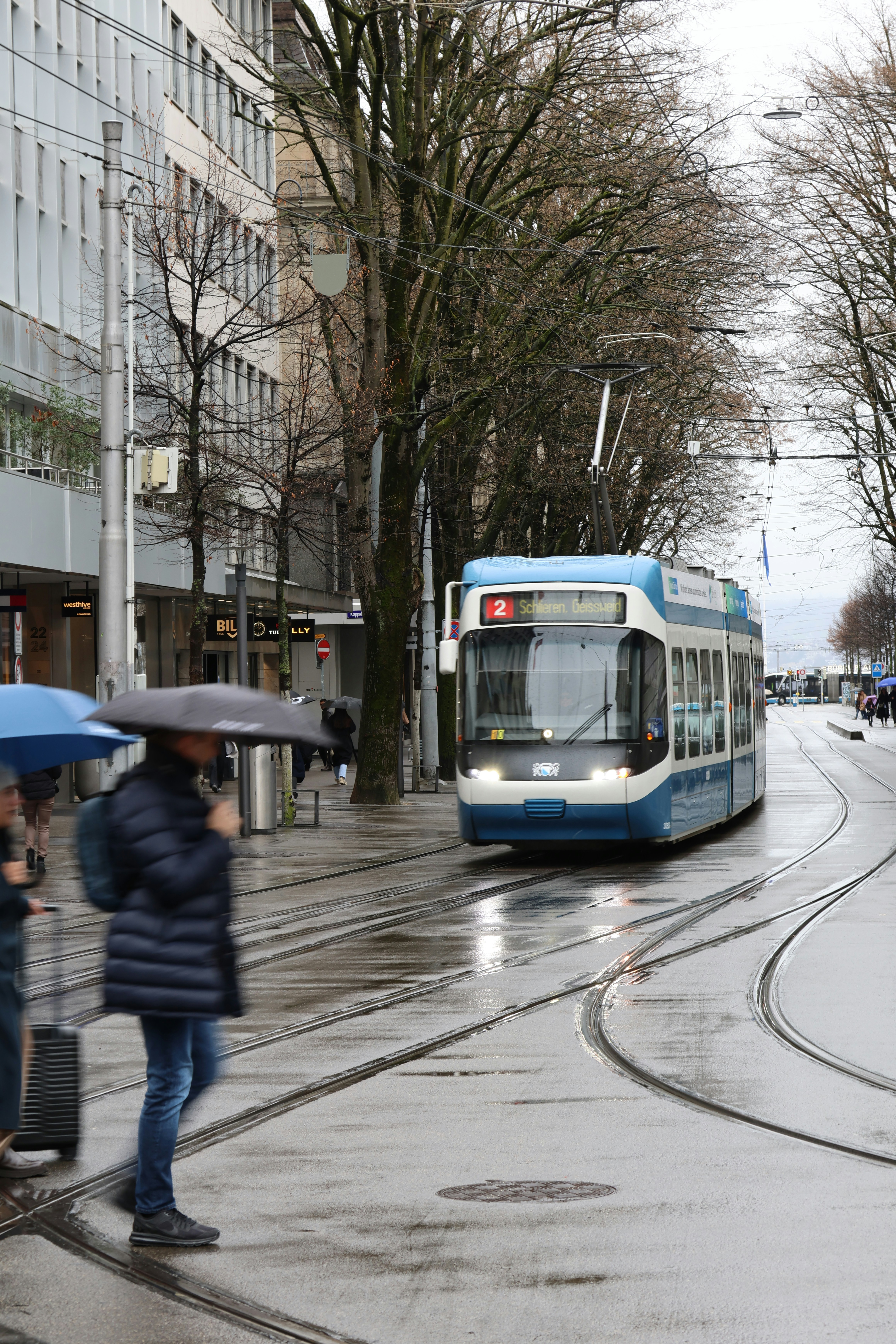 Blue Tram Rounds the Wet City Street as Shoppers Step Lightly