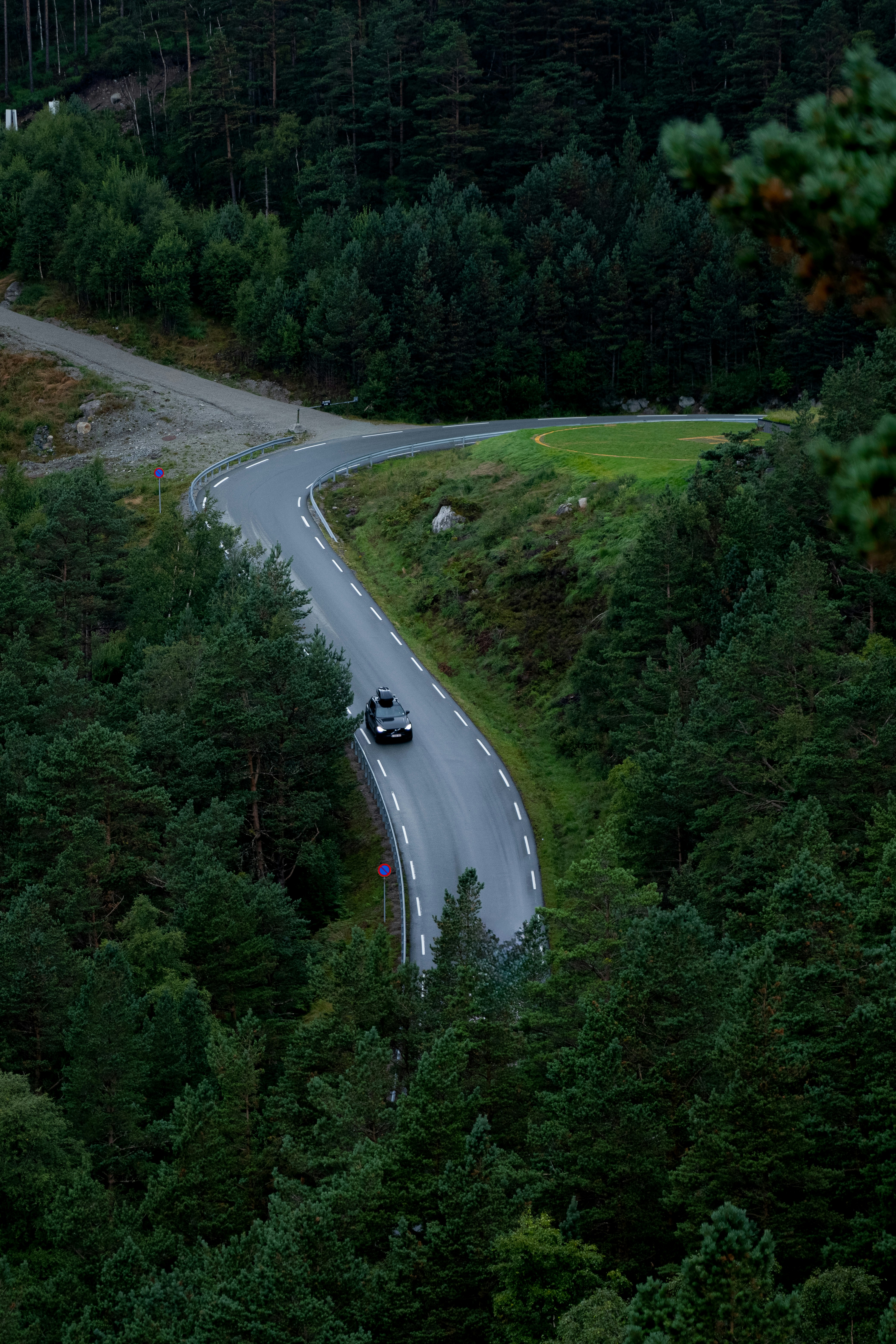 Curved Descent: A Lone Car Navigates a Misty Forested Curve