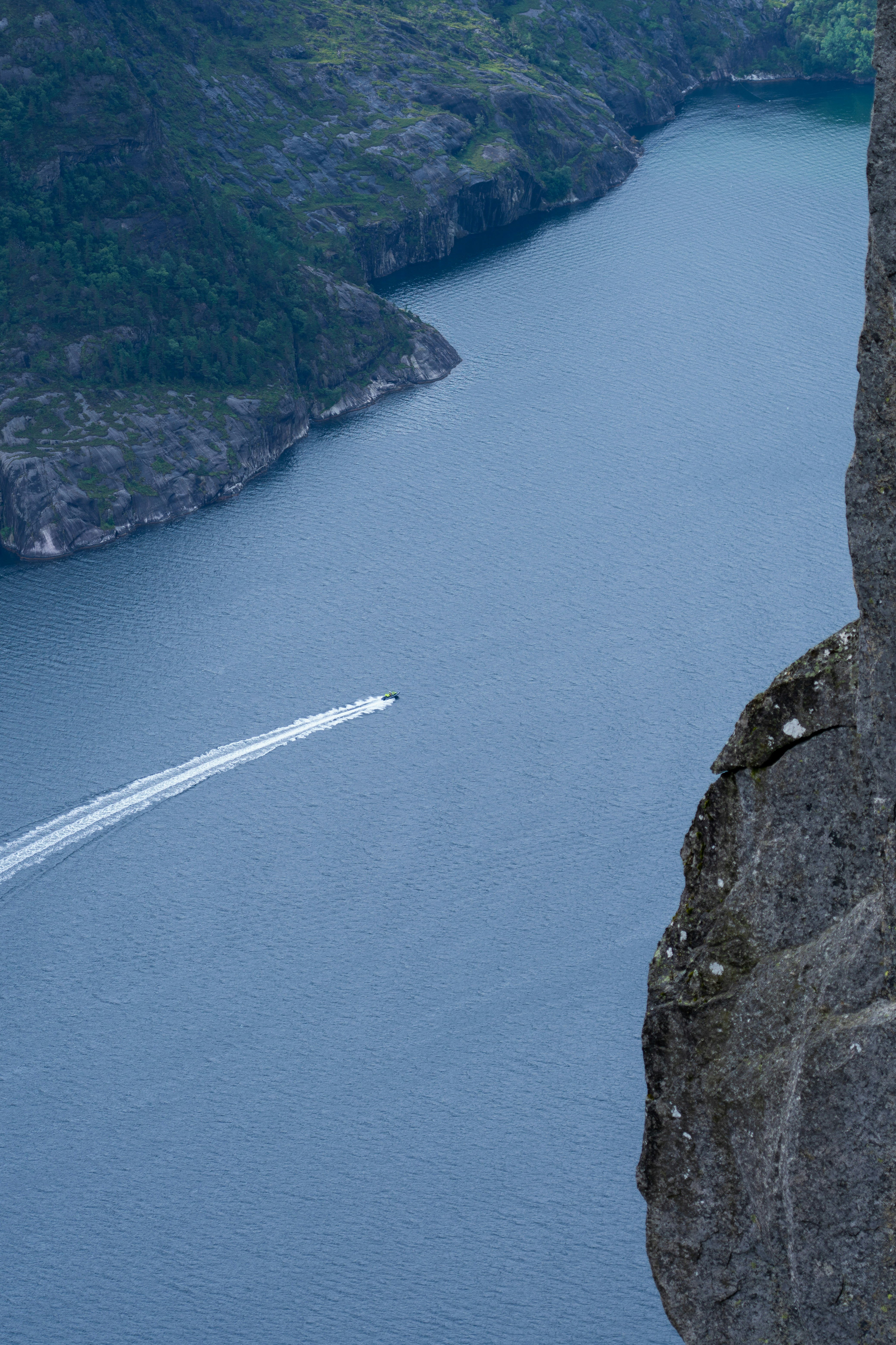 Cliffside Overlook: A Boat Slicing Through Fjord Blues