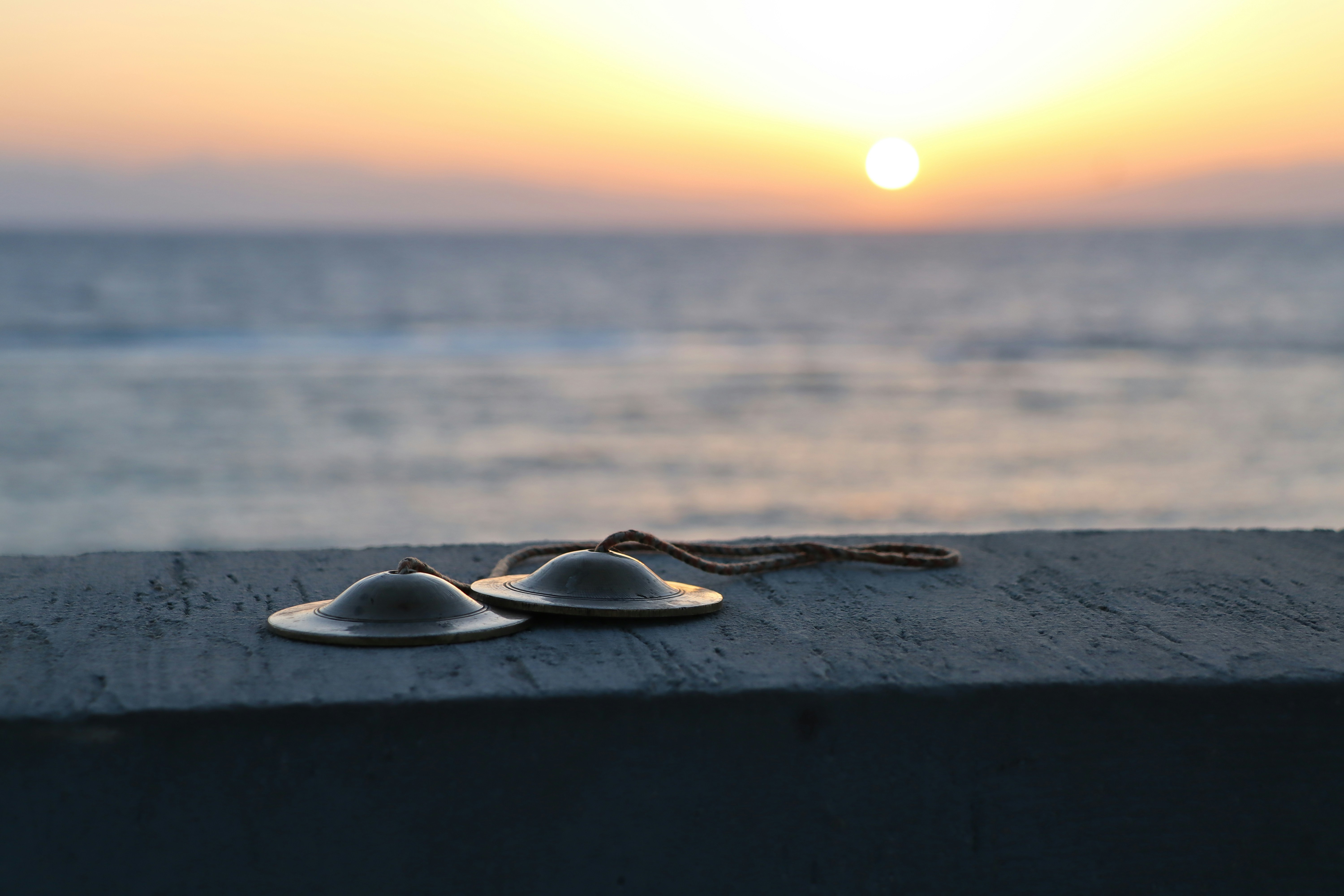 Sunset over a calm sea with a weathered railing in the foreground; metal suction-cup-like objects rest on the railing, creating a simple still-life against the luminous horizon.