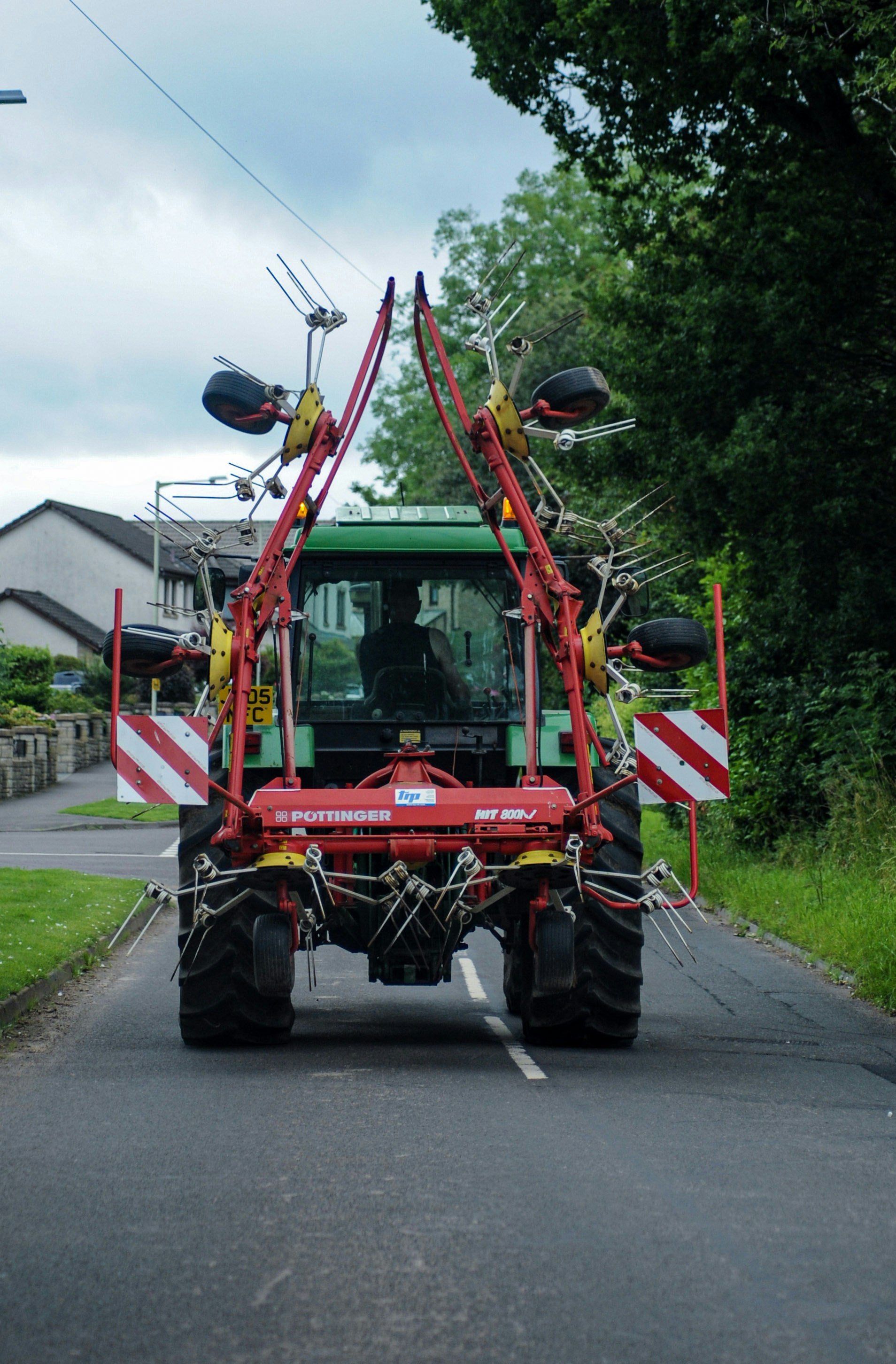 Rear View of a Red Pottinger Agricultural Trailed Implement on a Narrow Rural Road