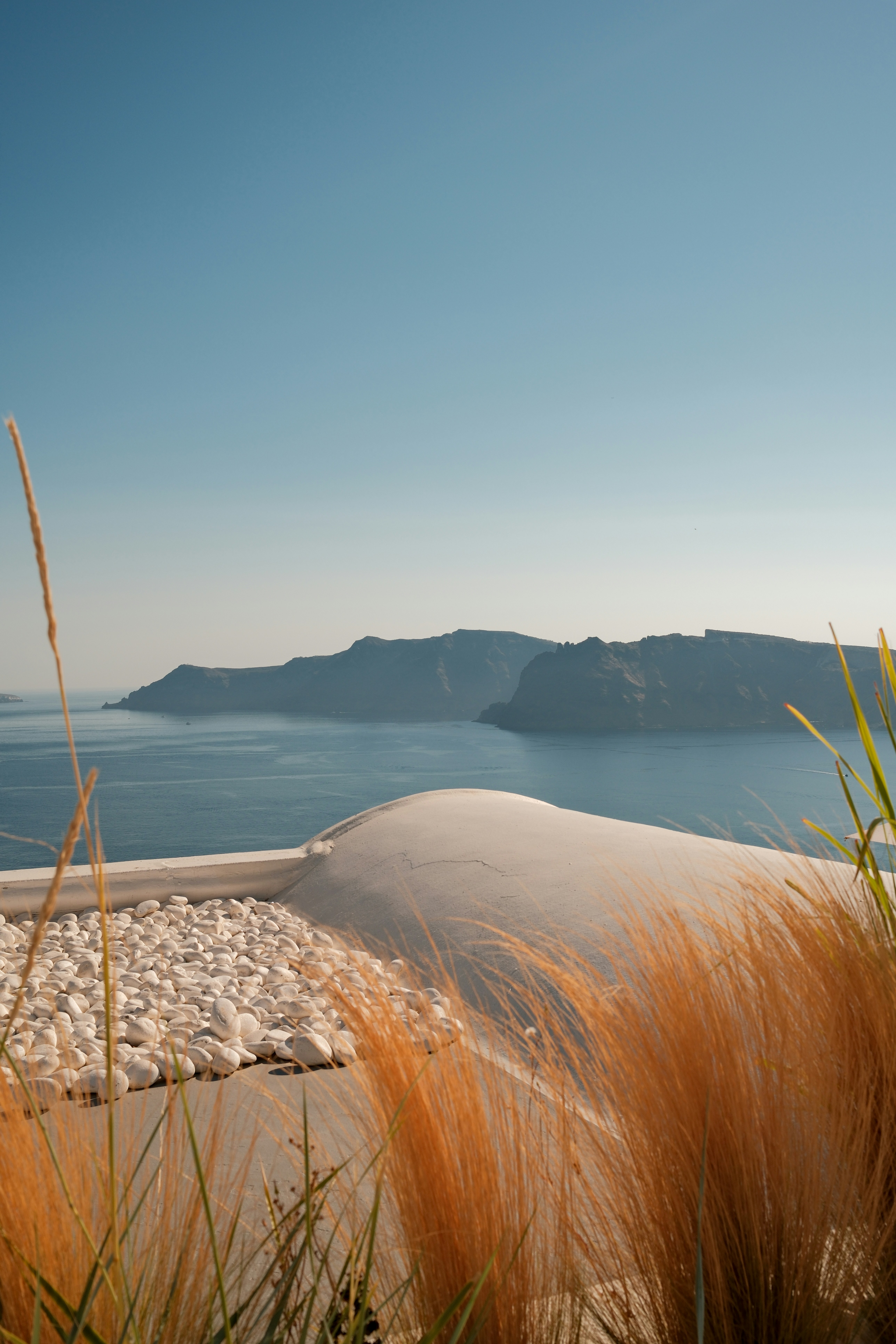 Santorini silhouette: sea, cliff, and seaside grasses fringing a sunlit terrace