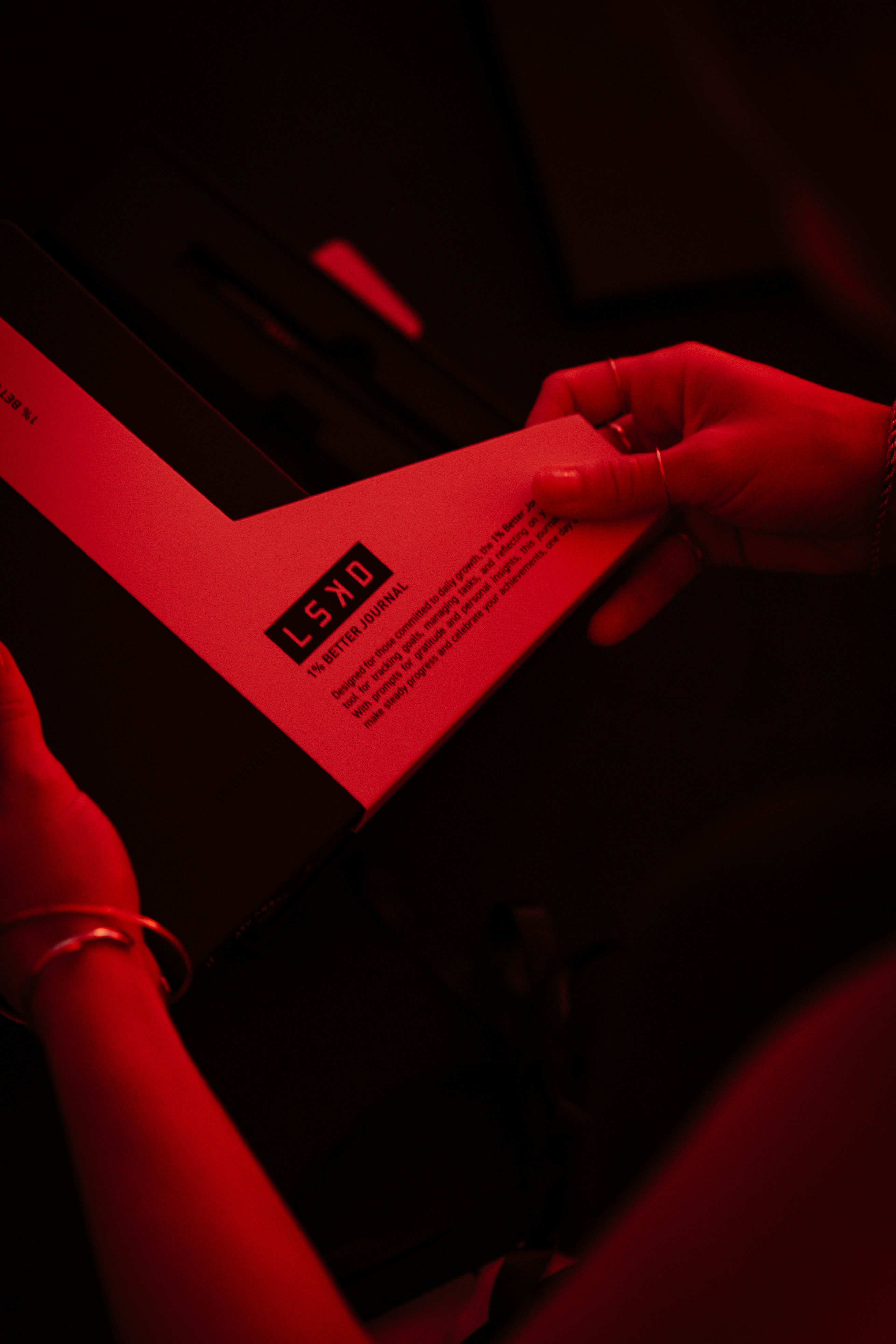 Red-lit hands fold open a card-like booklet
