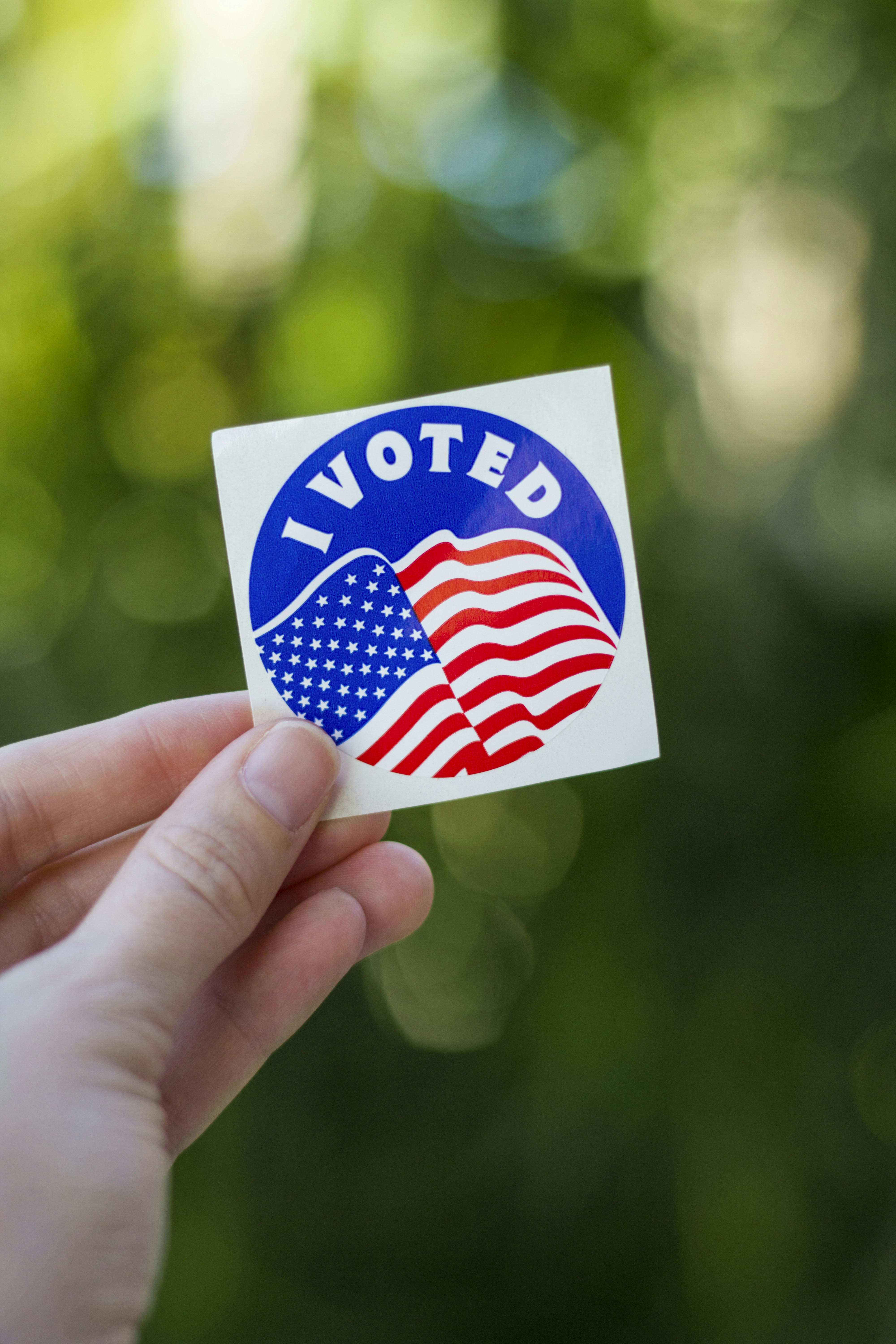 Sticker of a Voted Card Held Against a Blurred Green Backdrop