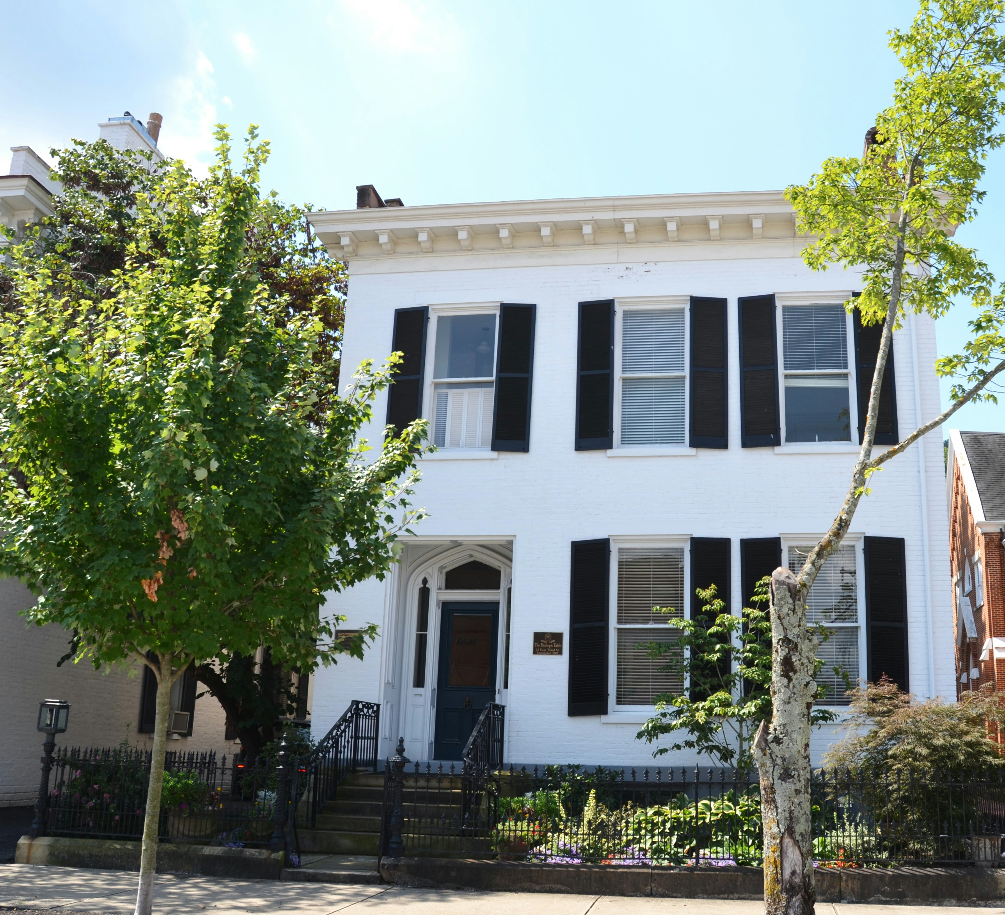 White façade with black shutters: a sunlit townhouse framed by trees
