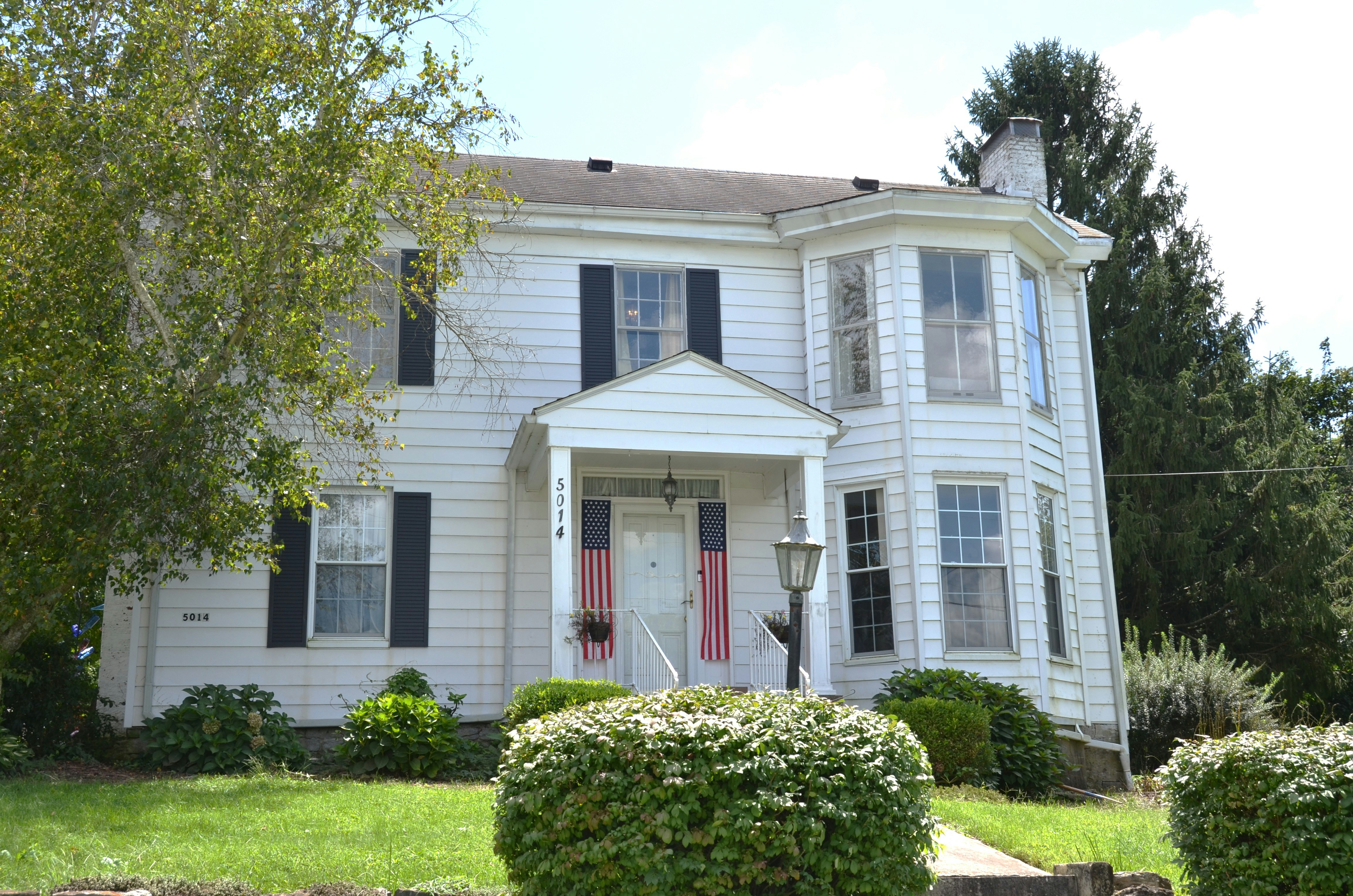 Front Facade of a White Victorian-style House with Shaded Lawn and Flags