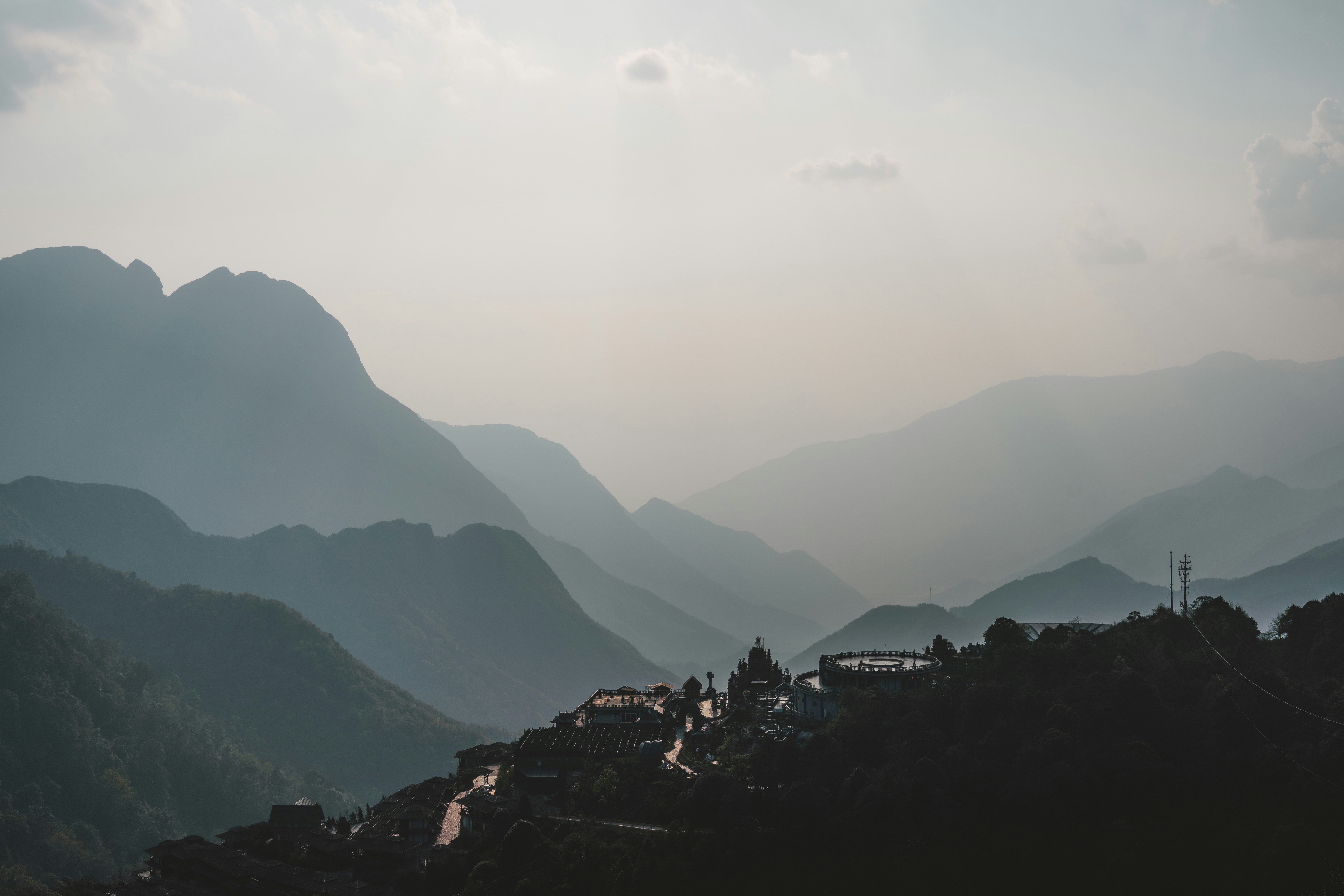 Terraced village clings to a ridge beneath layered mountain silhouettes as soft light washes the valley.