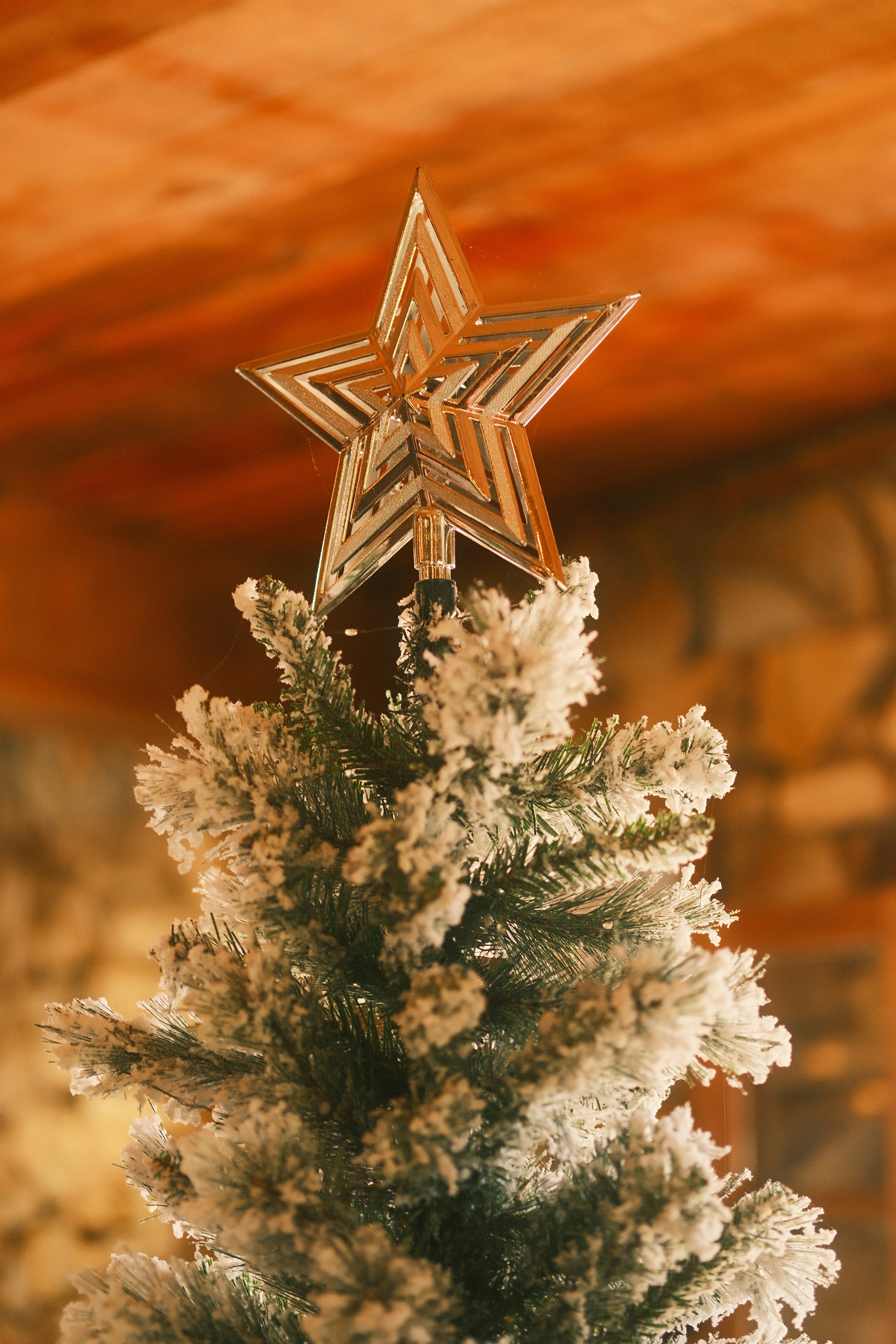 Star atop a snow-dusted Christmas tree in a warm, rustic interior