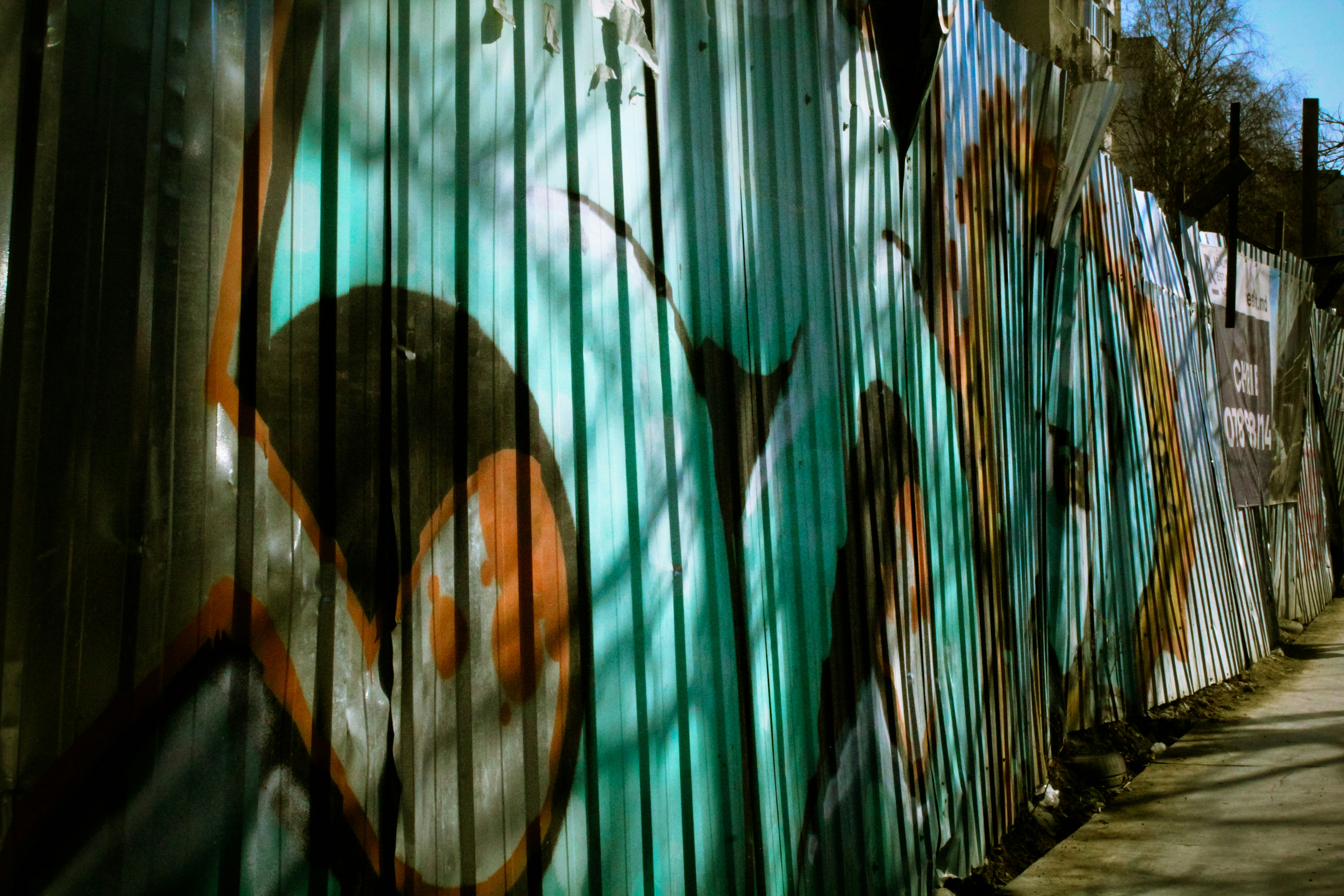 Colorful graffiti walls run along a sunlit alley, with corrugated metal panels forming a textured, mural-covered corridor.