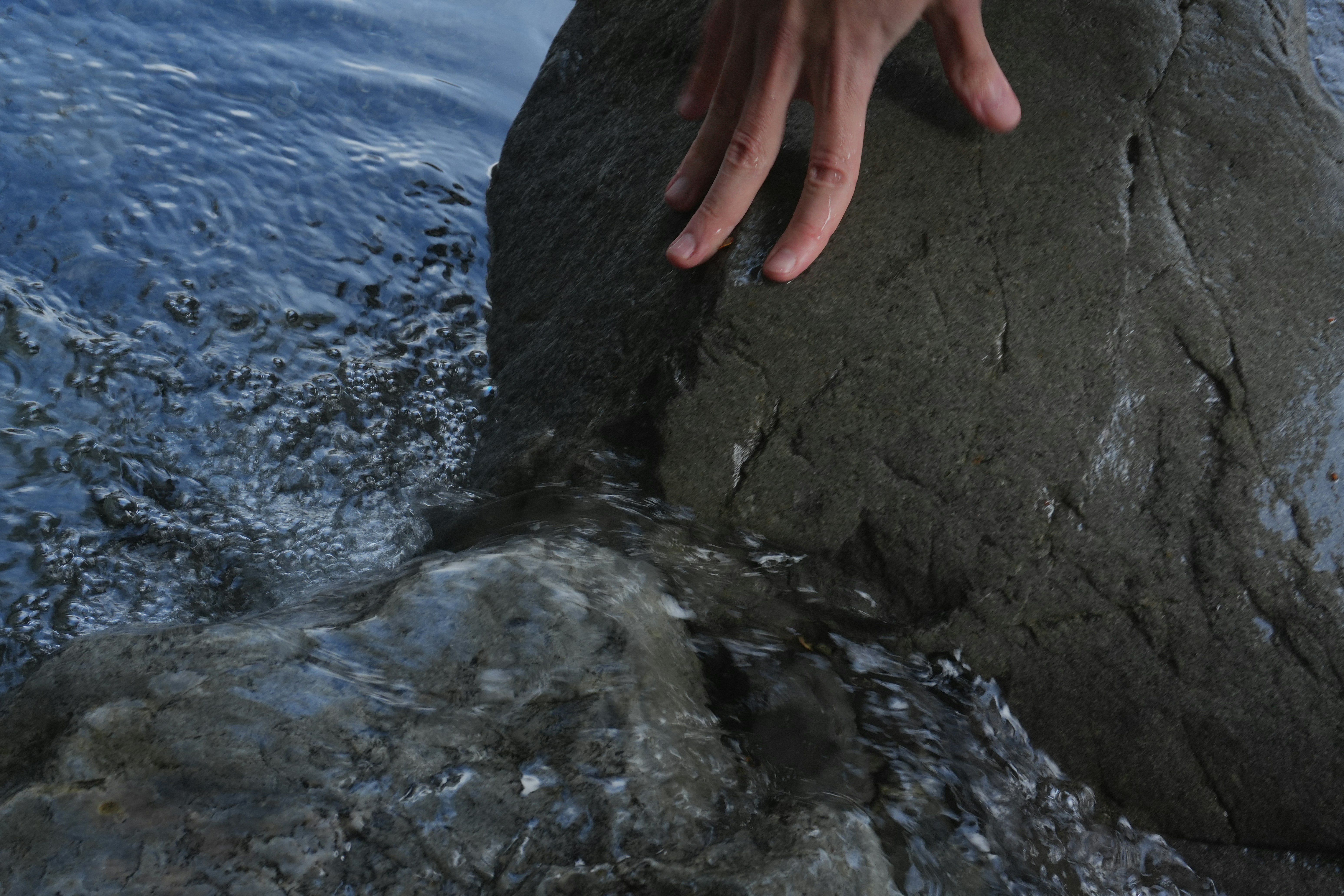 Stillness at the Rivulet: a hand resting on jagged rock by flowing water