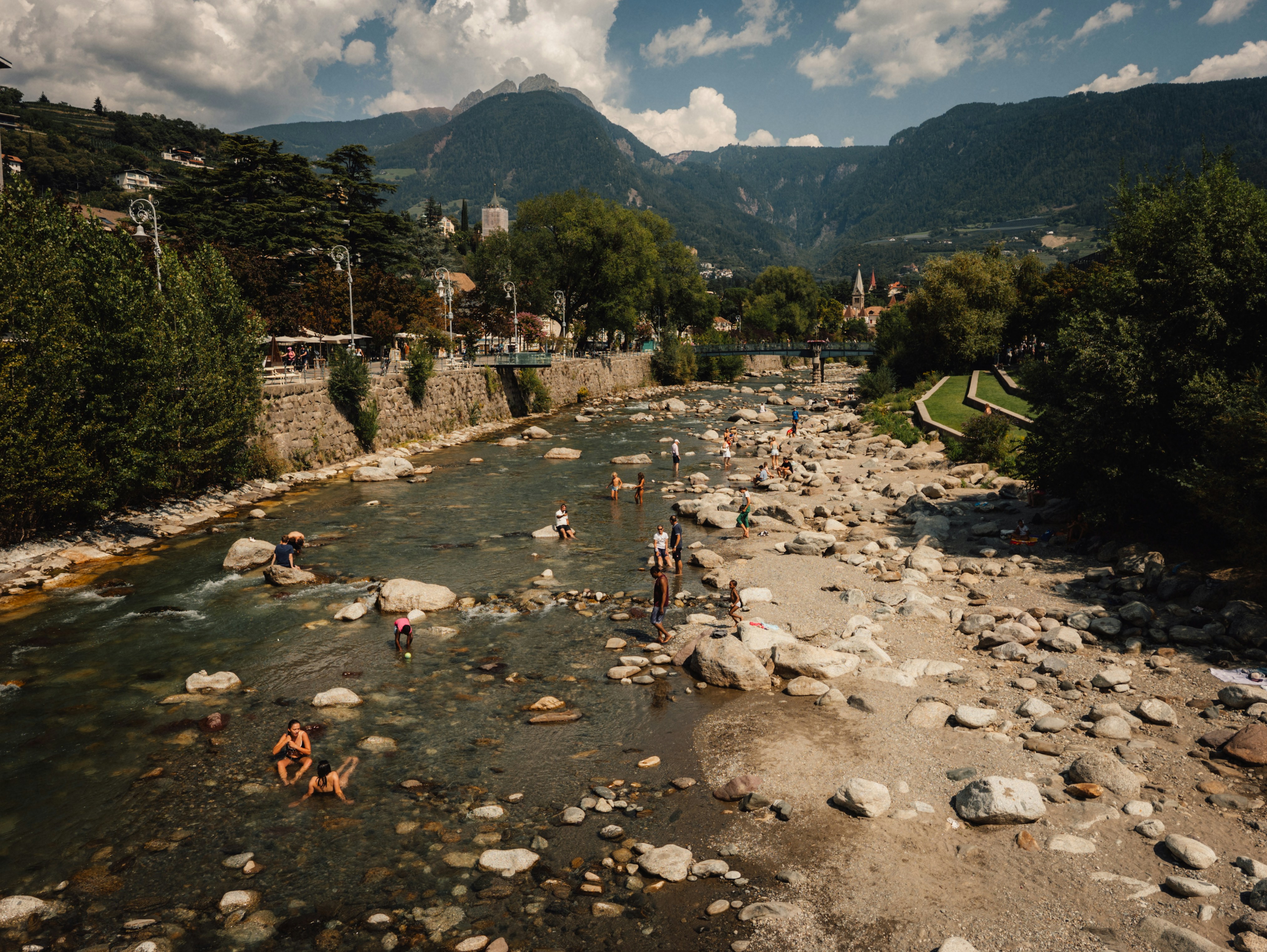 Riverwalk in Alpine Light: People Wading Along the Rocky Stream