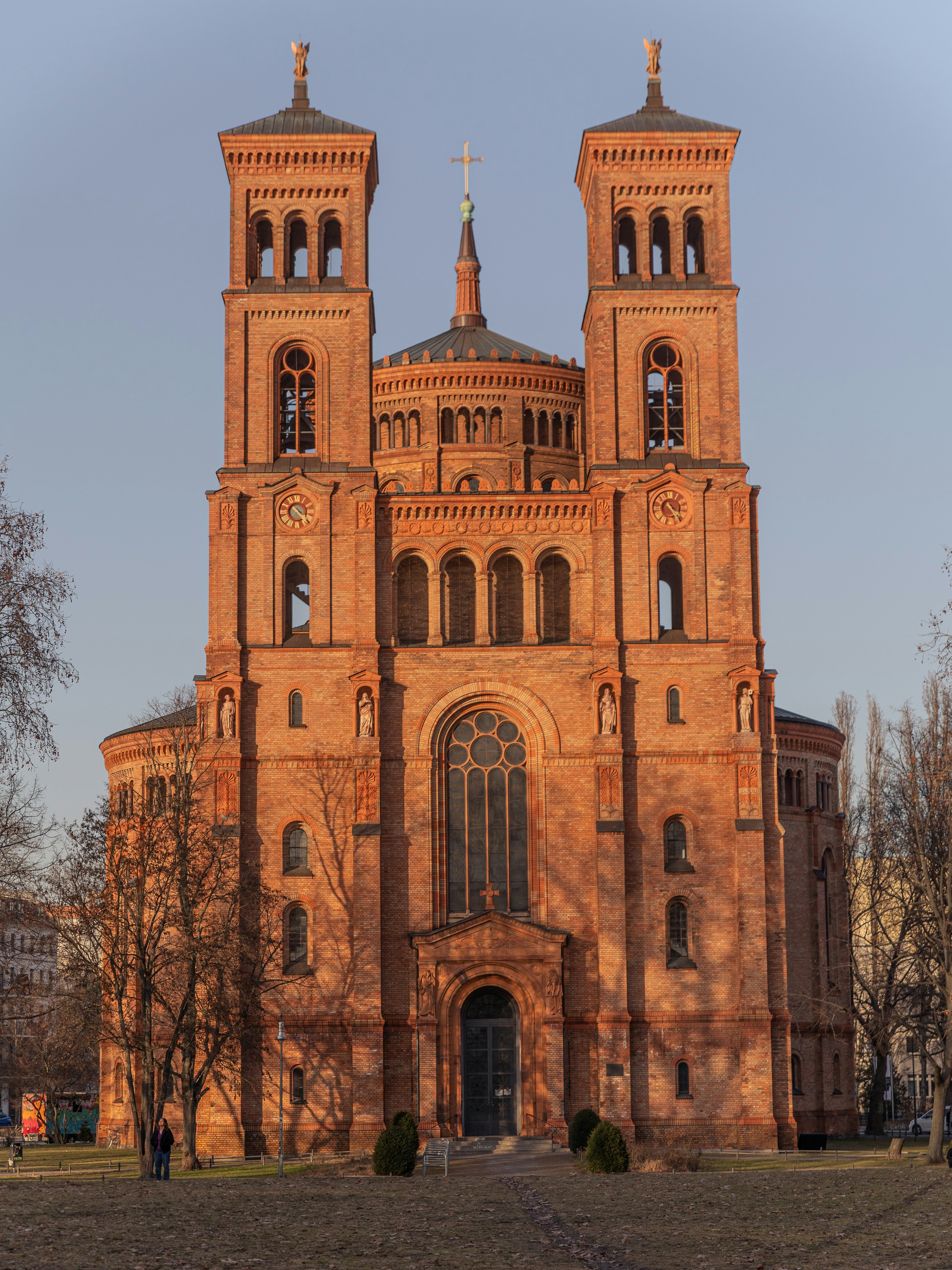 Brick basilica with twin towers framed by bare trees, illuminated by warm sunset light.