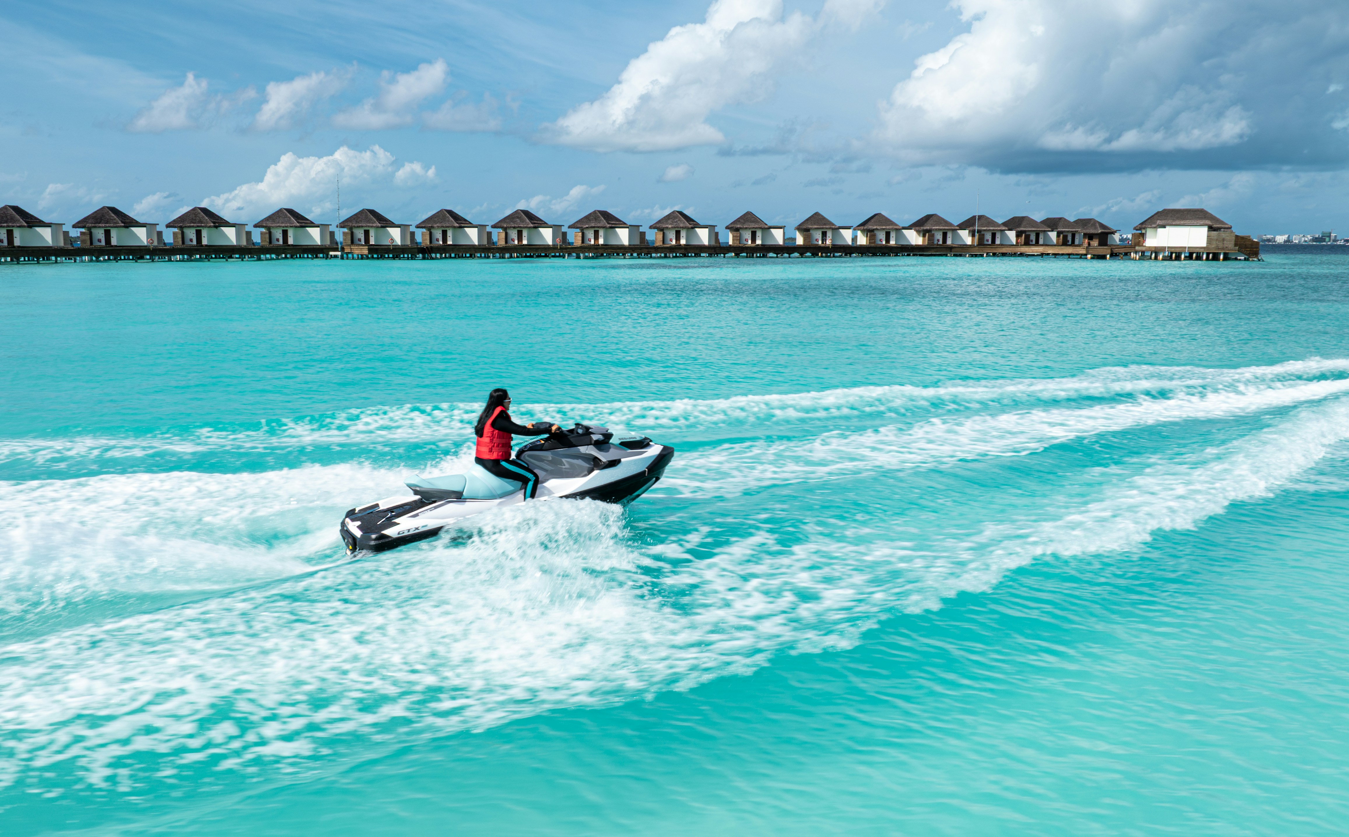 Jet-ski in turquoise lagoon: a lone rider carving white trails beneath overwater bungalows