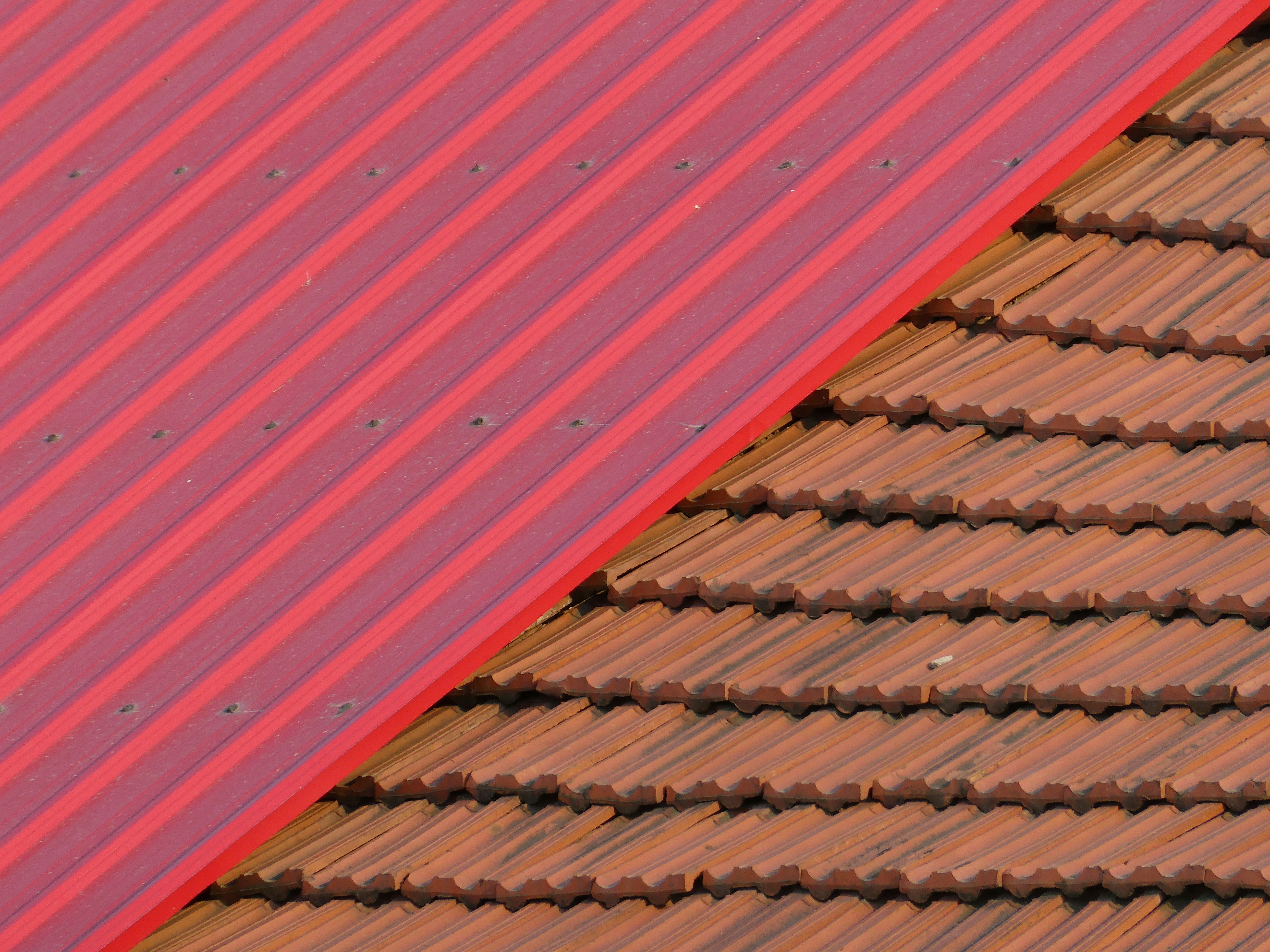 A bright red corrugated metal roof beside a brown clay tiled roof