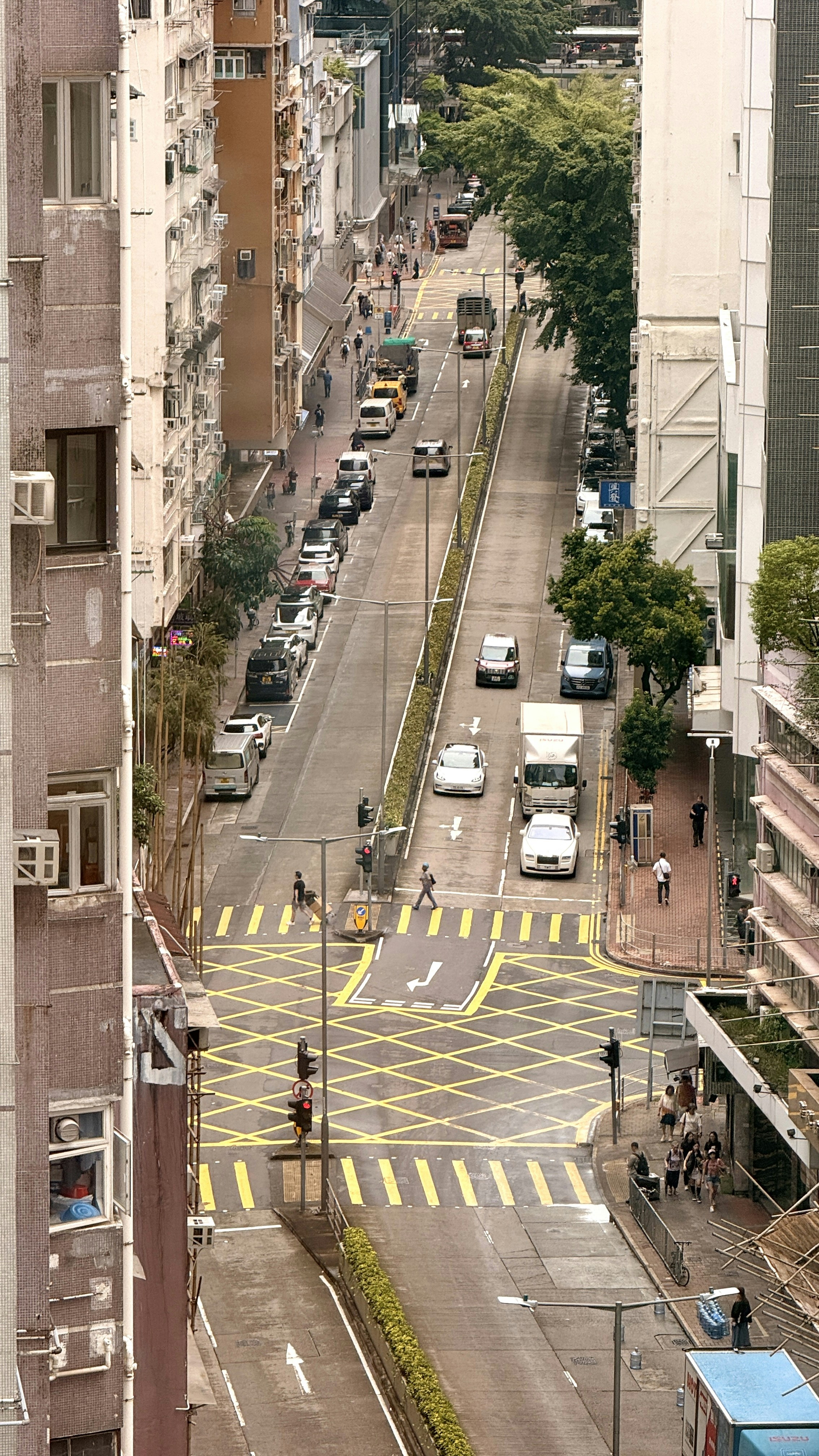 Urban street scene with a tall, narrow view showing crosswalks, vehicles, and pedestrians lined between apartment buildings; clearly a street-level urban landscape with marked pedestrian zones and traffic flow.
