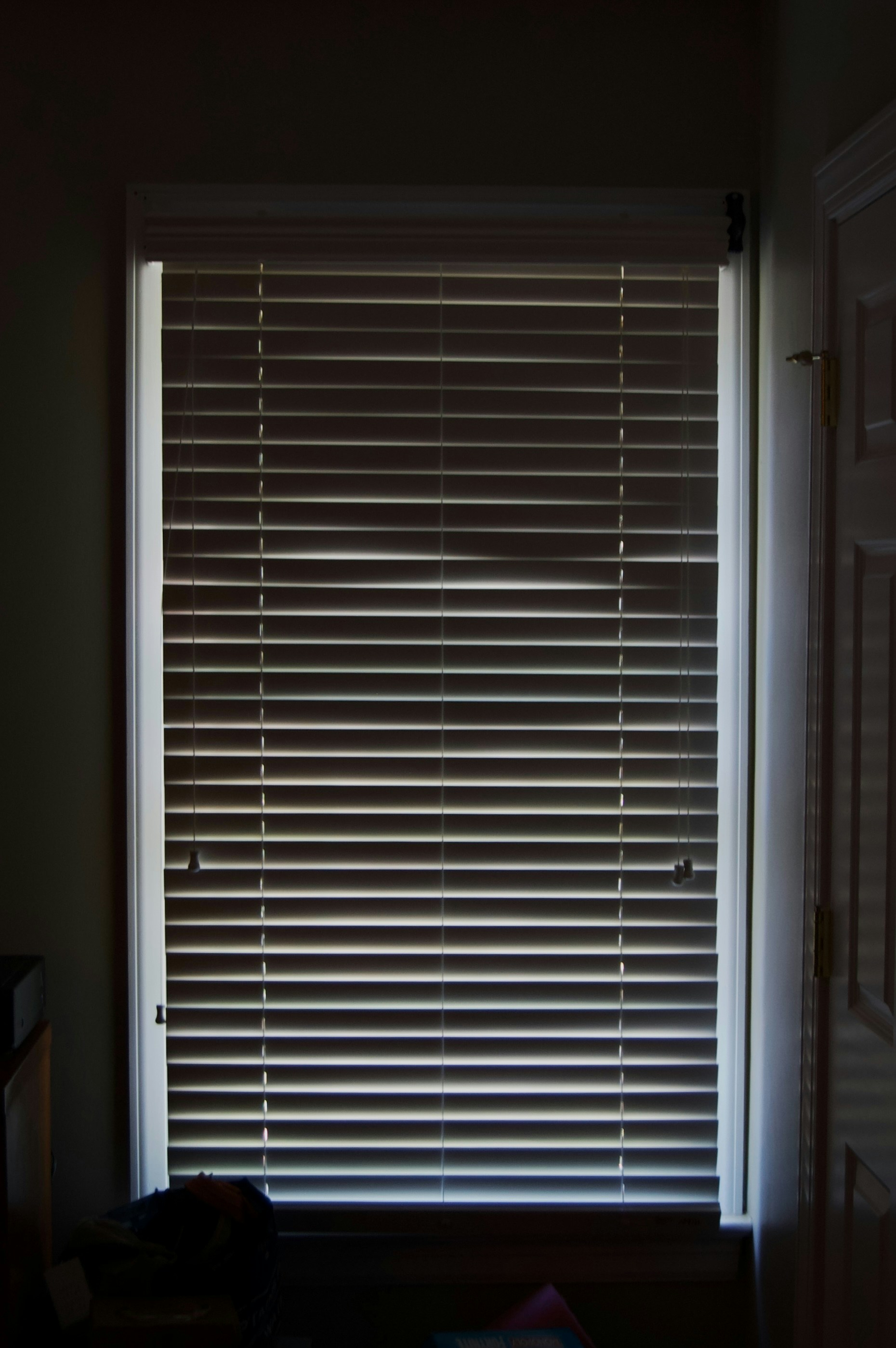 Slatted blinds flood the doorway with a narrow beam of light in a dim interior.