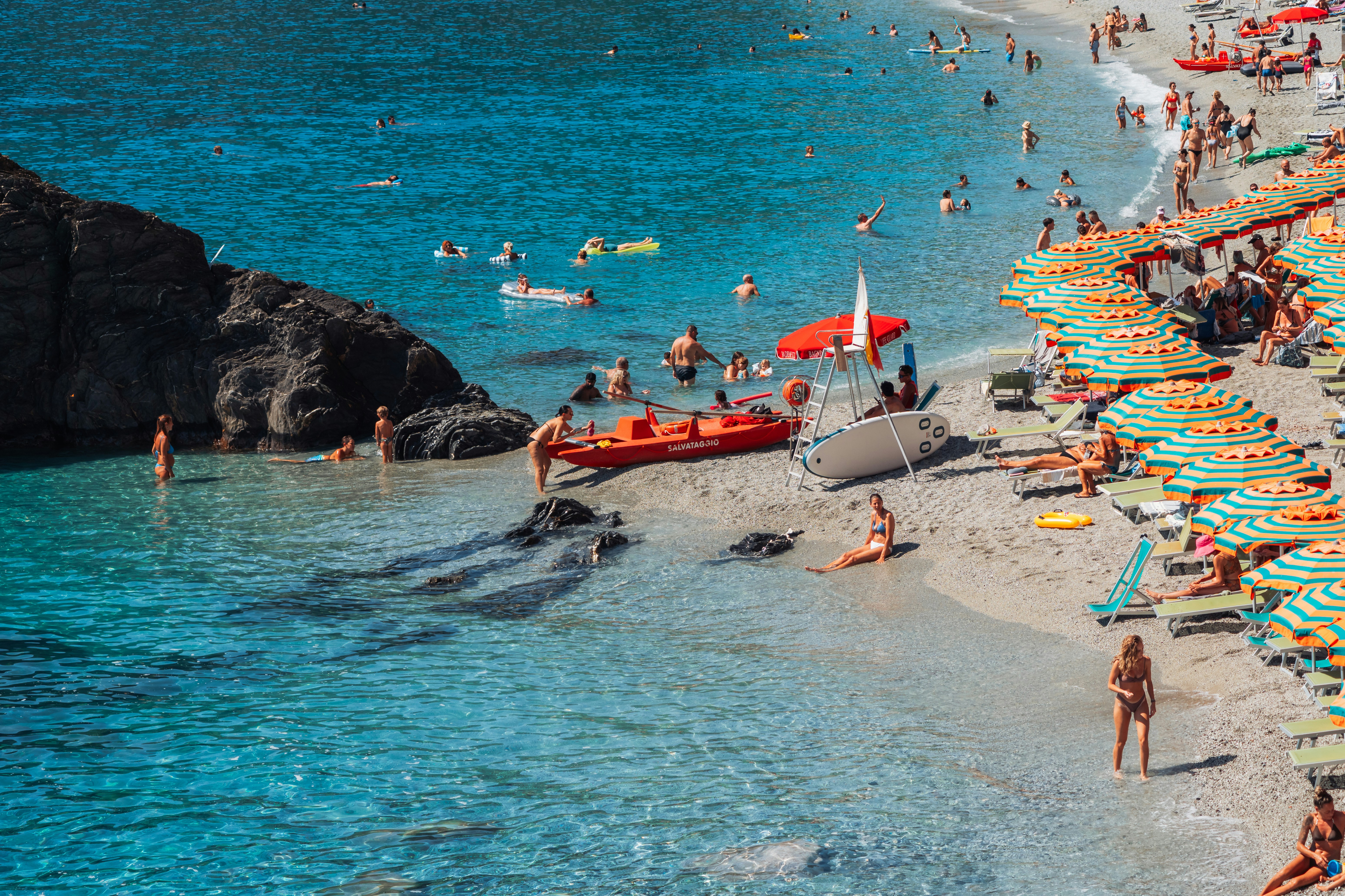 Sunlit Strand: Boats, Umbrellas, and a Crowded Crescent
