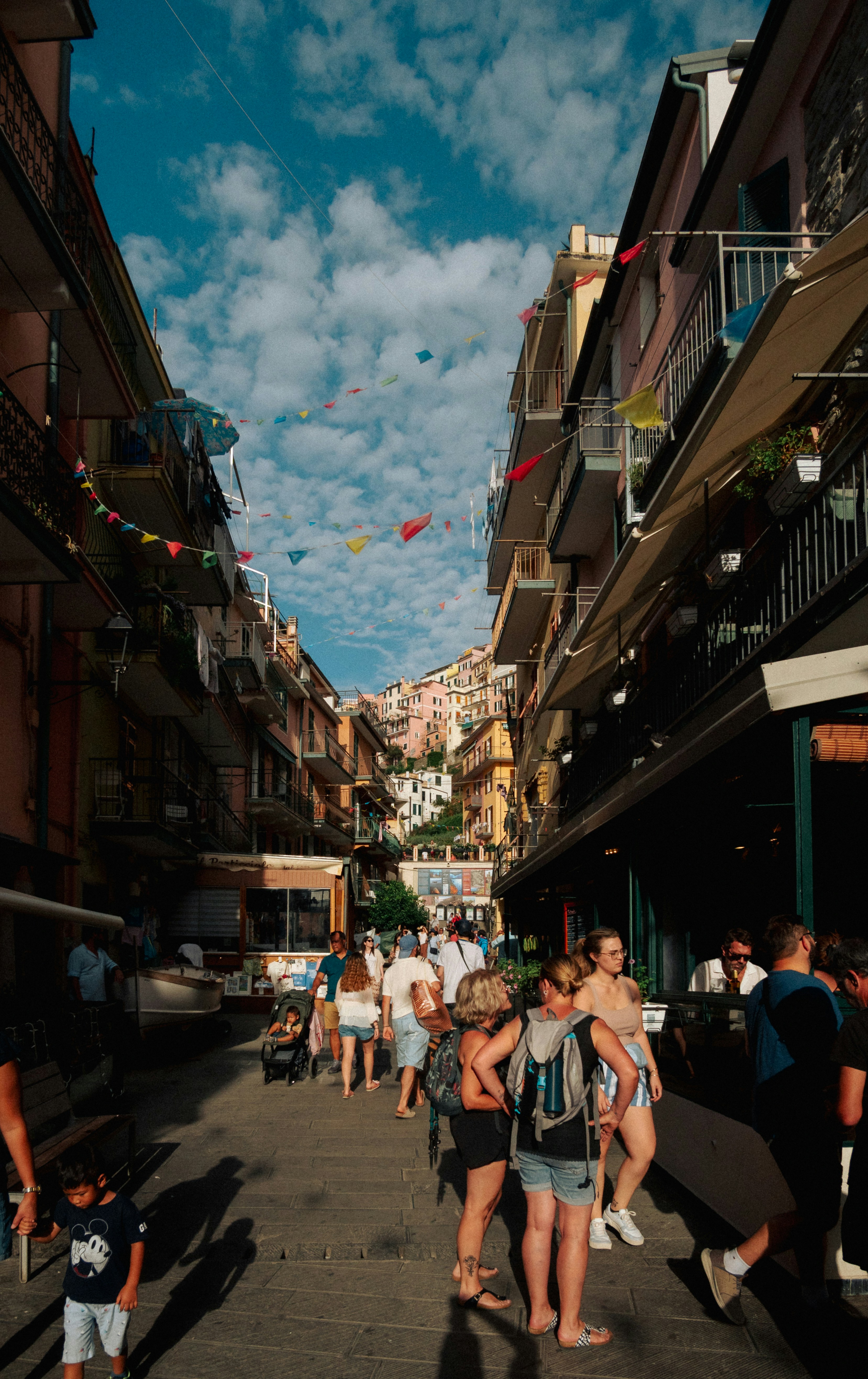 Coastal uphill street festival: colorful banners and a gathered crowd beneath sunlit balconies