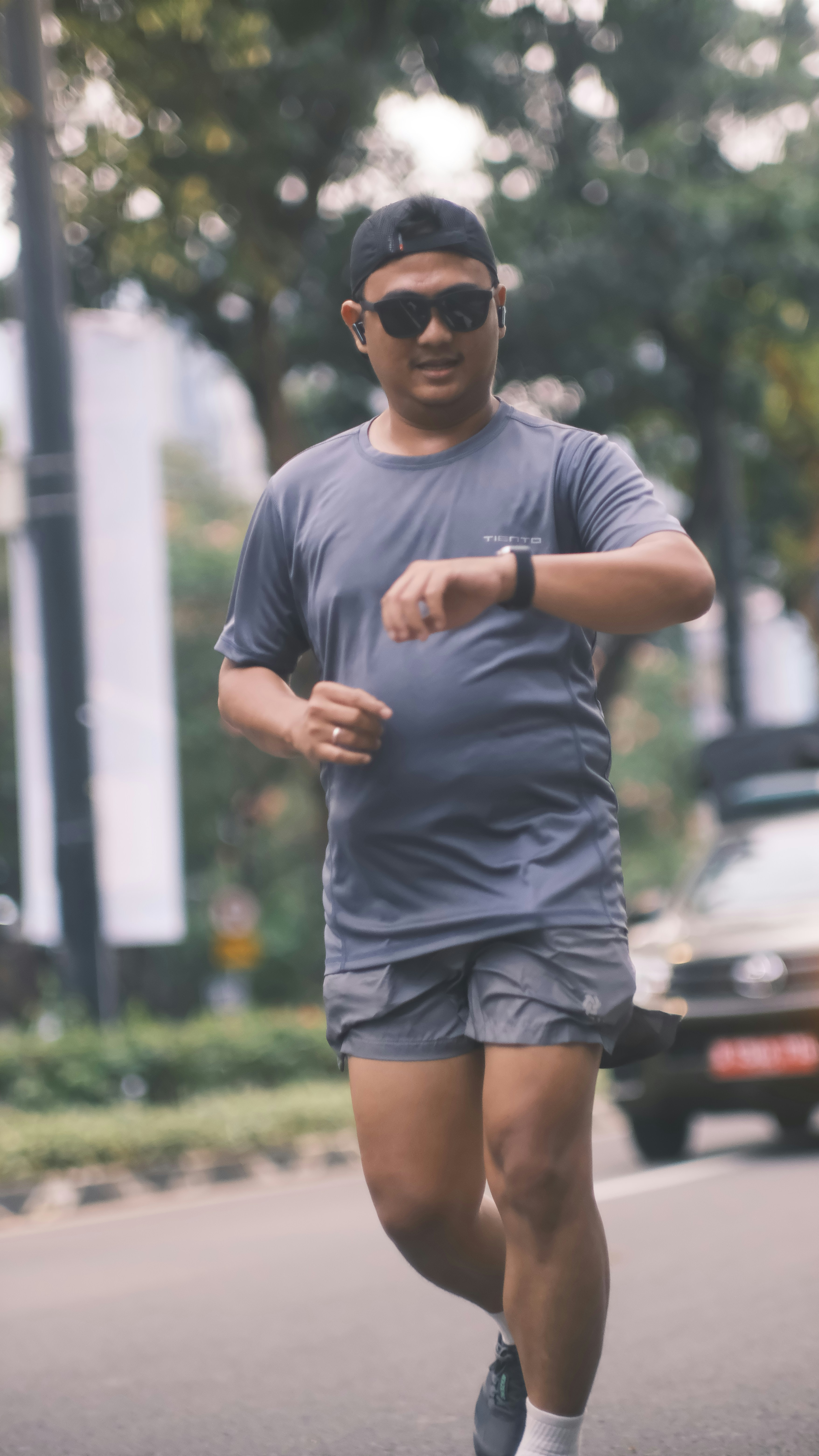 Male runner in gray athletic wear sprints along a city street, with blurred background and subtle bokeh highlighting motion.