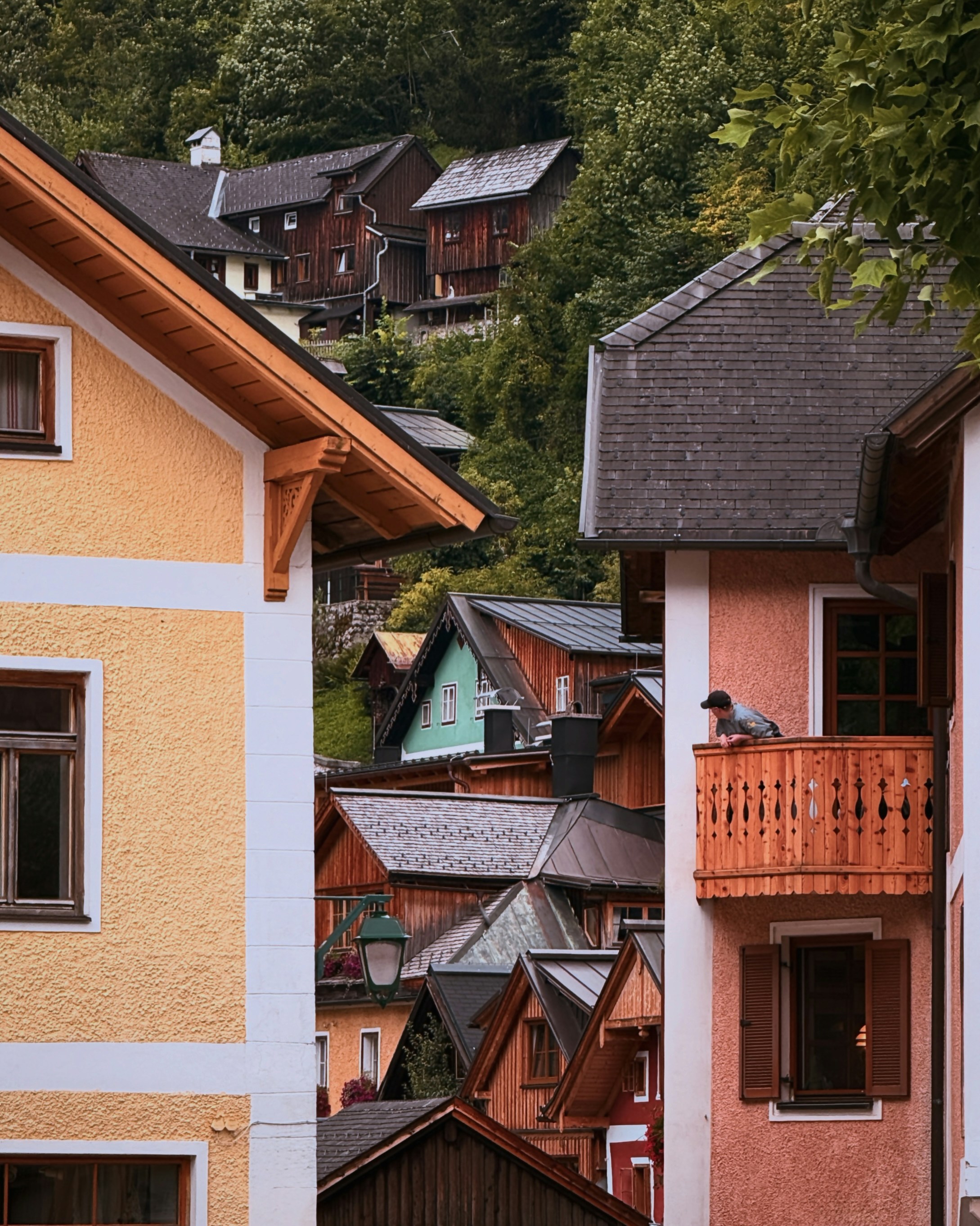 Colorful houses line a steep Alpine street with wooden balconies and sloped roofs, a quiet residential scene in a mountain village.