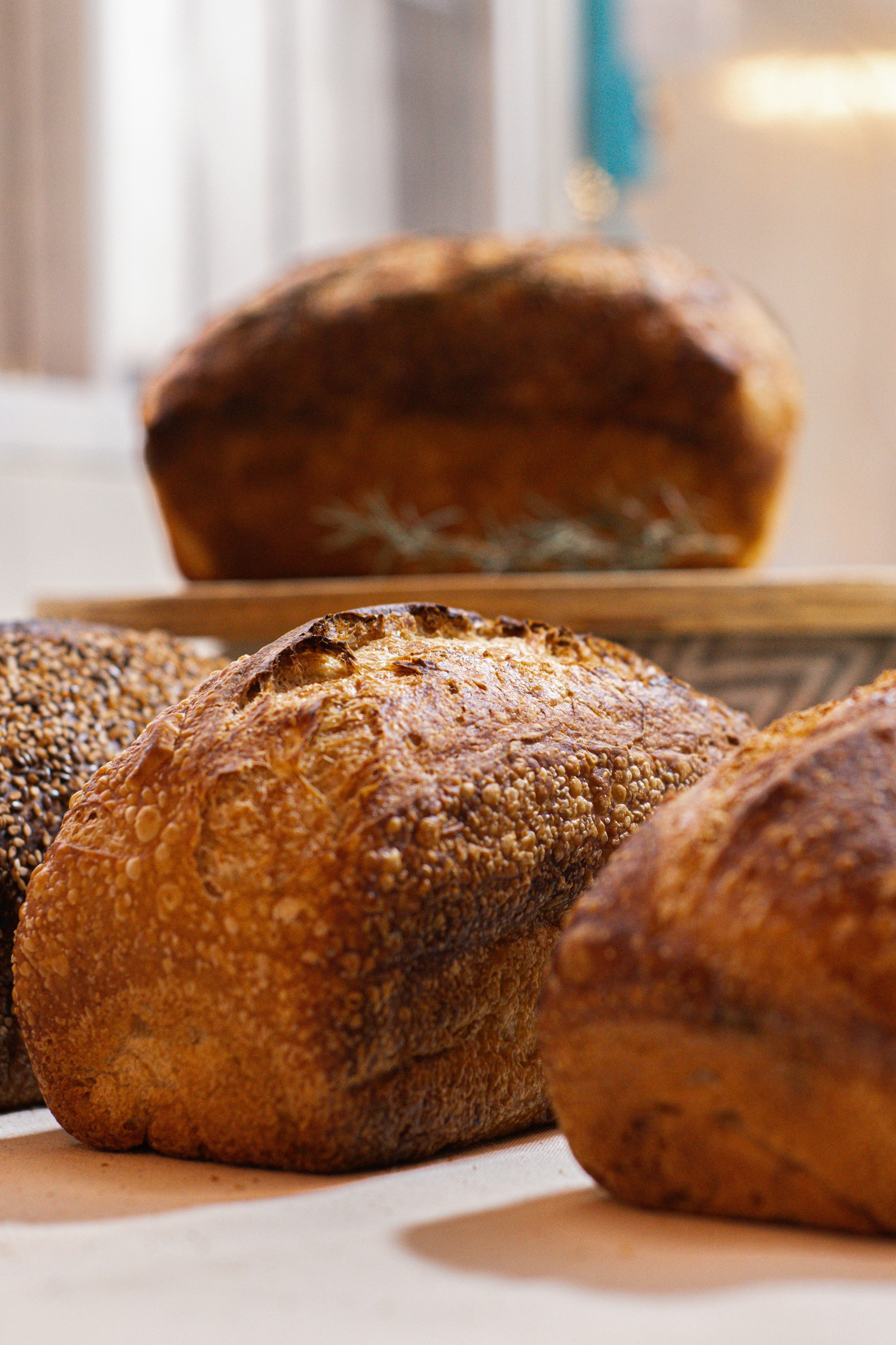 Close-up of rustic loaves with textured crusts resting on a wooden surface, showcasing artisanal bread in a warm kitchen setting.
