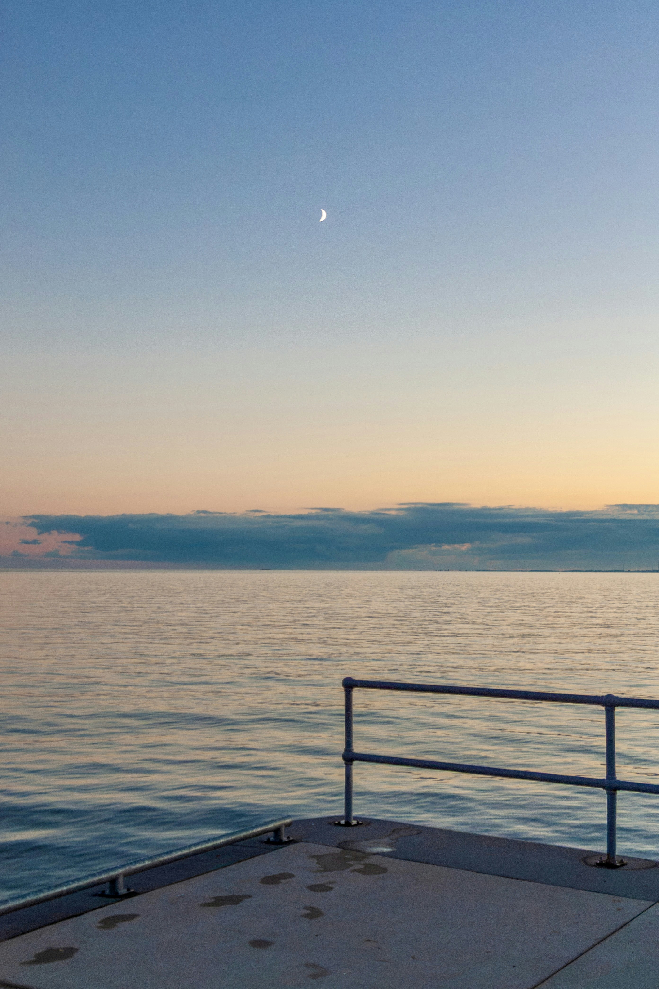 Dawn over the Pier: Crescent Moon over Calm Waters