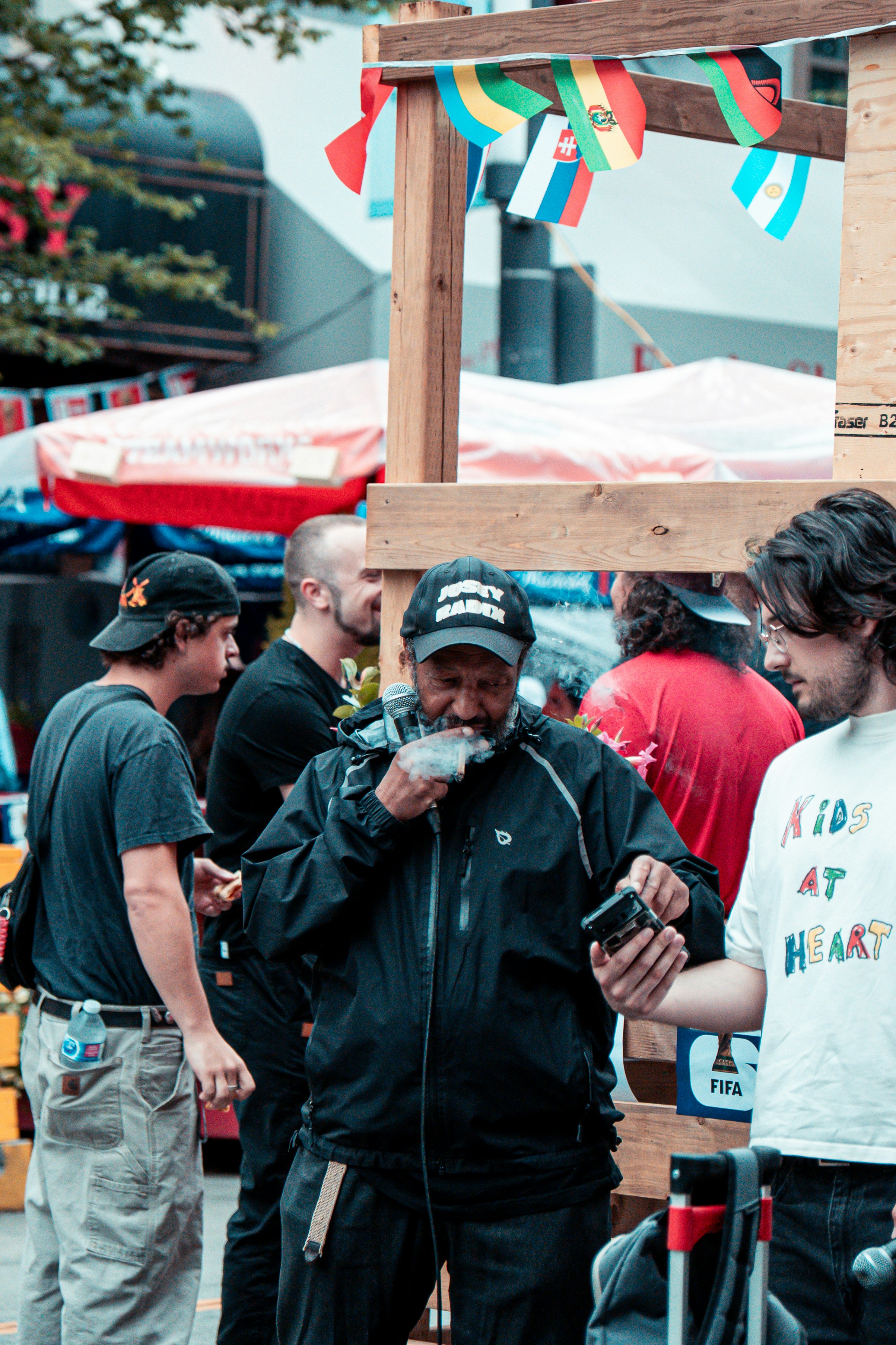 Vape Break at a Street Festival: A Man in Black Exhales as Friends Gather