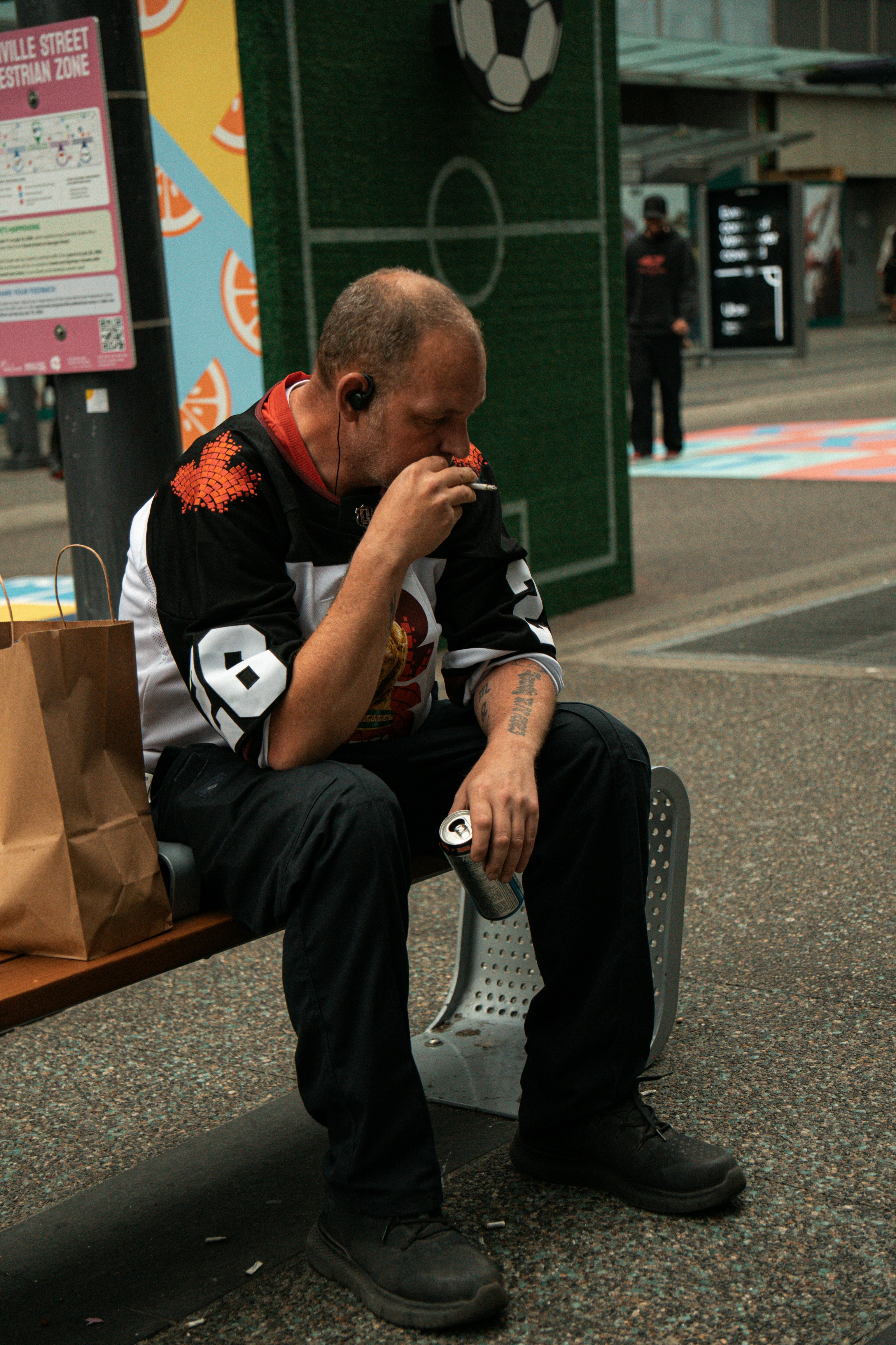 Man in a sports jersey resting on a bench at a city plaza