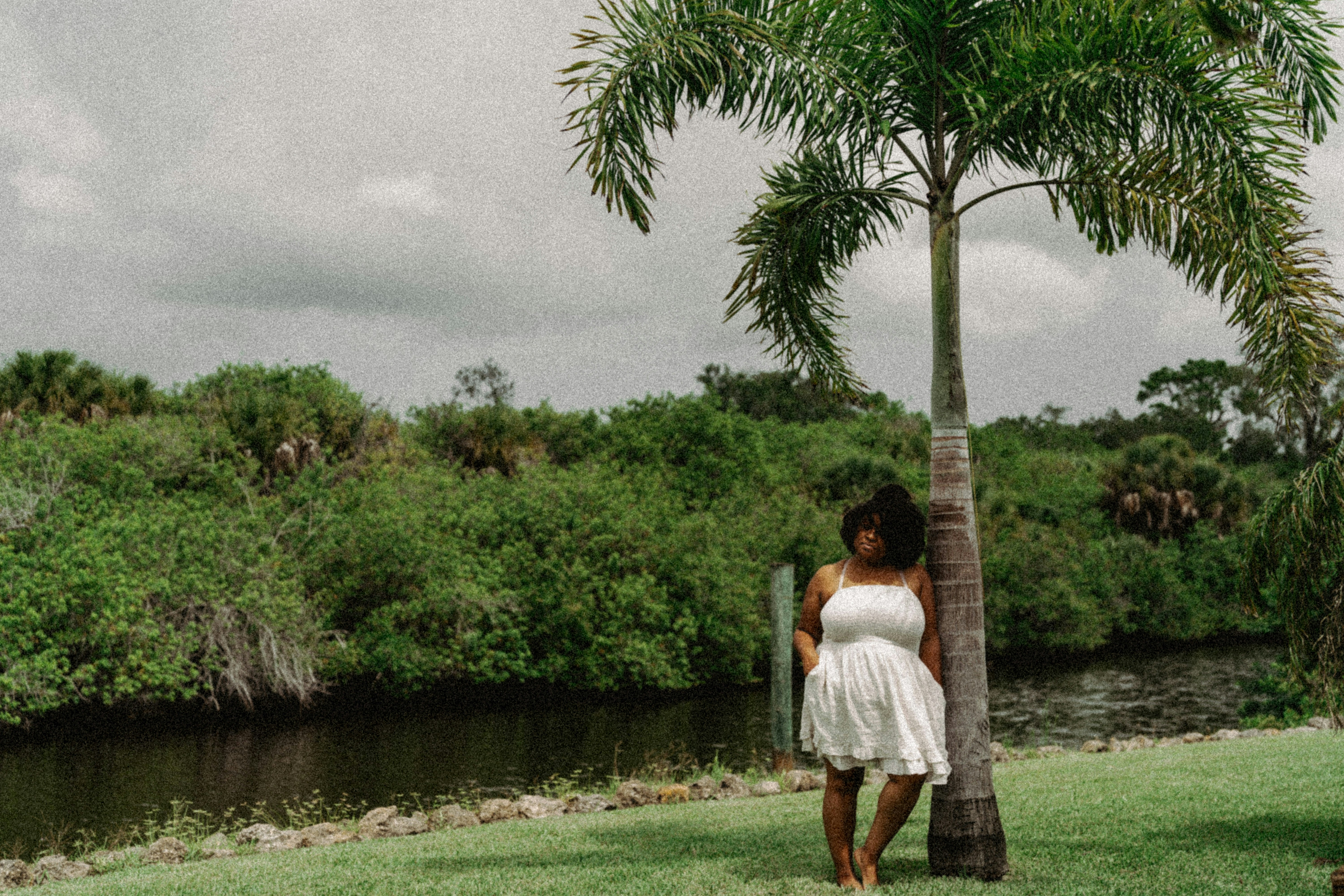 Sunlit Crescent: A Woman in White By the Riverside Palm