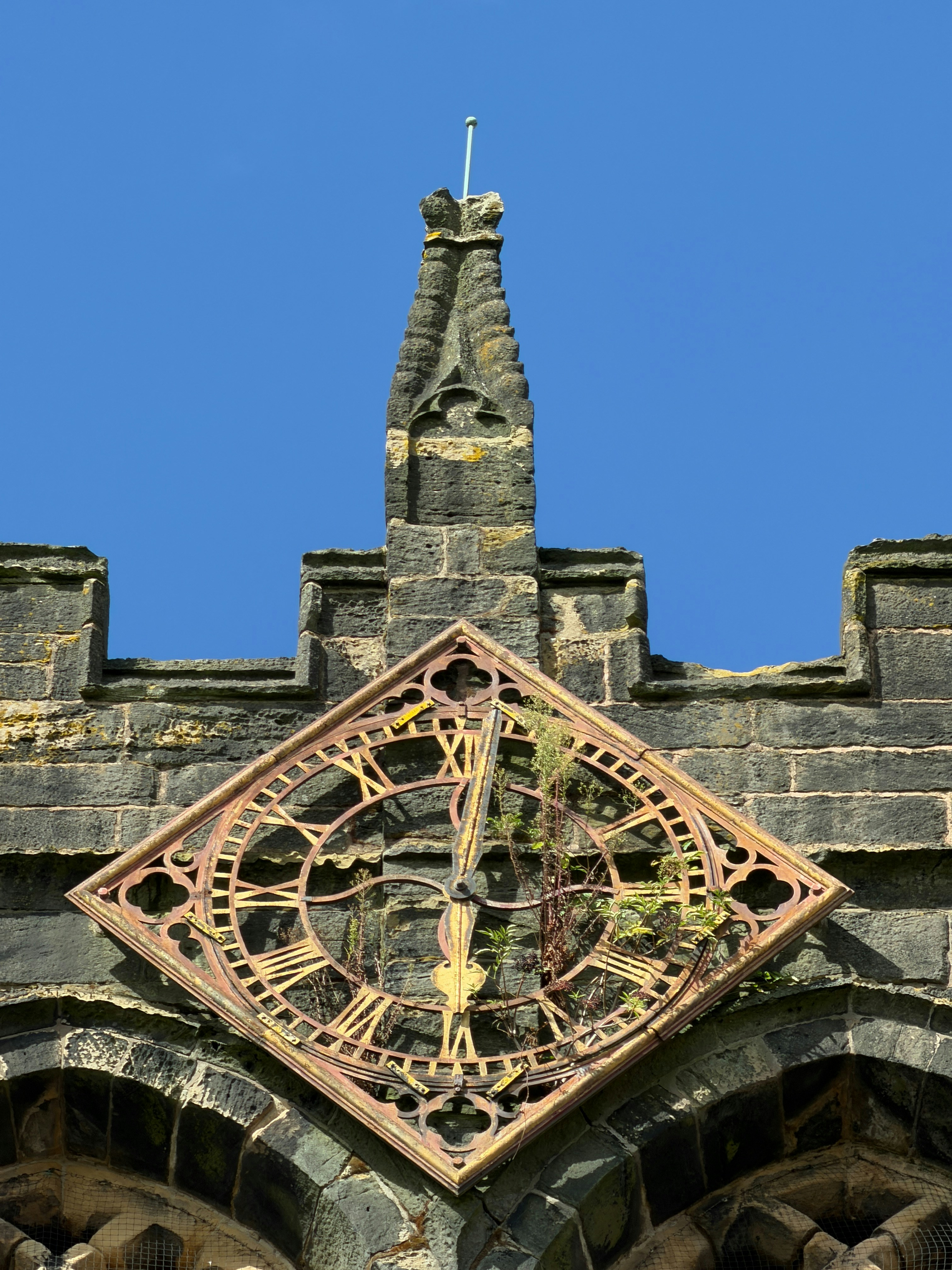 Angled Clock Face set into Stone Gables under a Clear Blue Sky