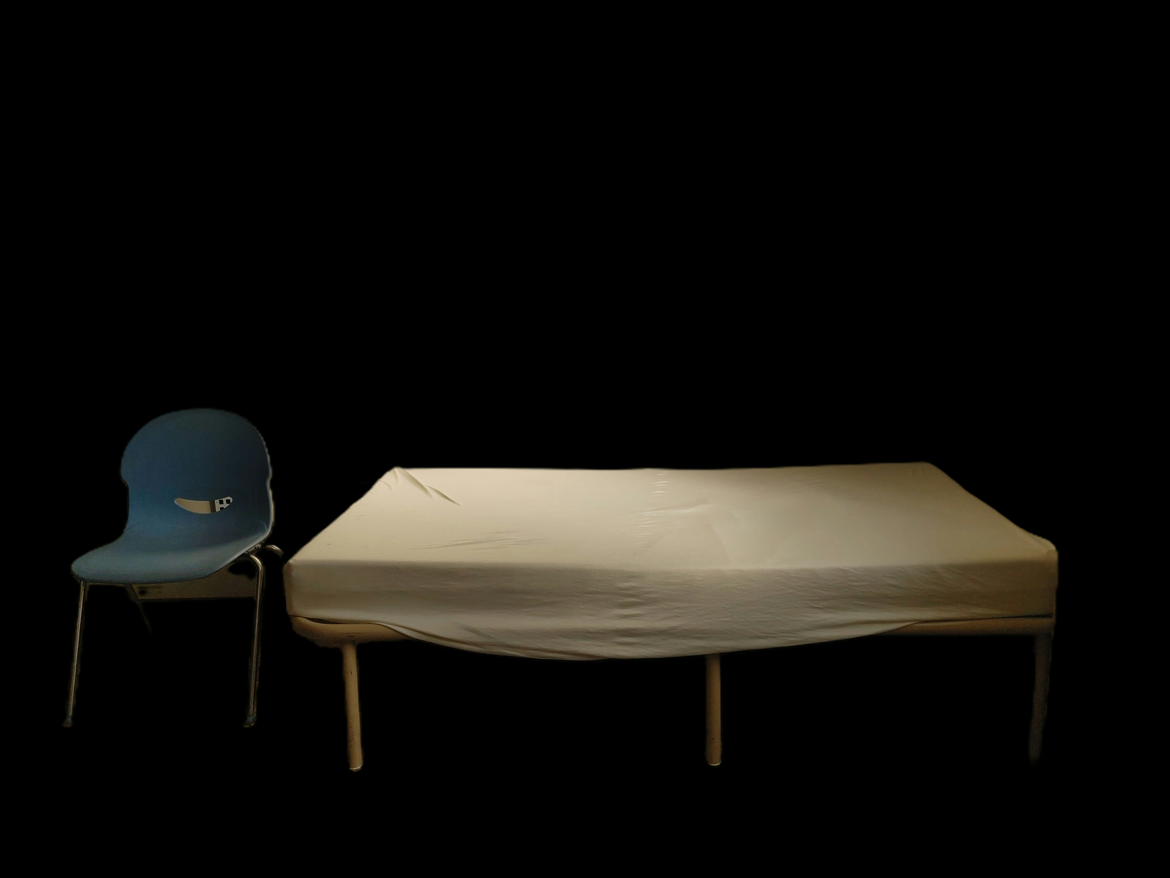 Blue chair beside a draped table set against a dark background; the space around suggests a staged scene or setup rather than a natural environment.