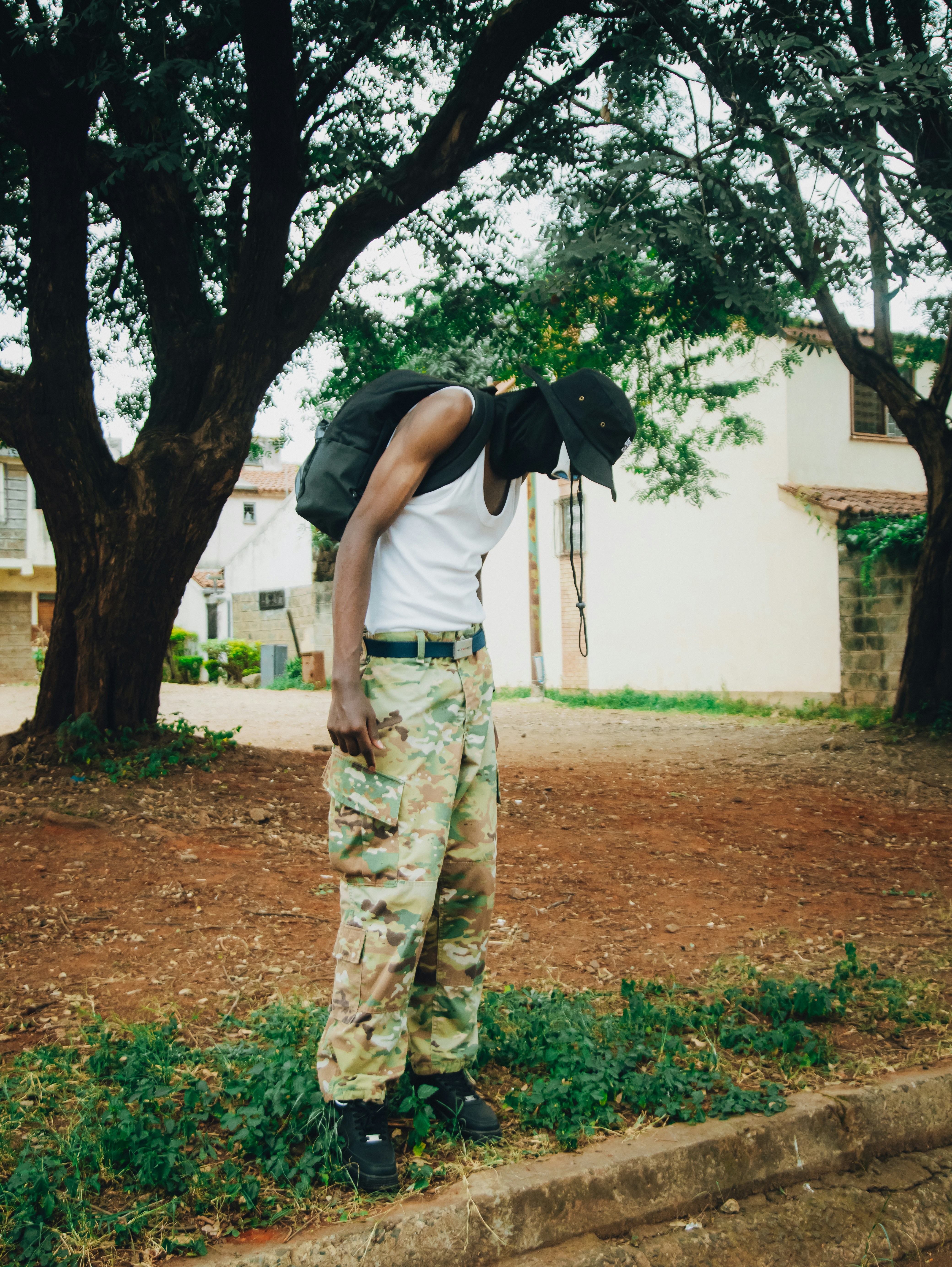 Traveler in camouflage stands under a shadowed canopy, tracing the path ahead