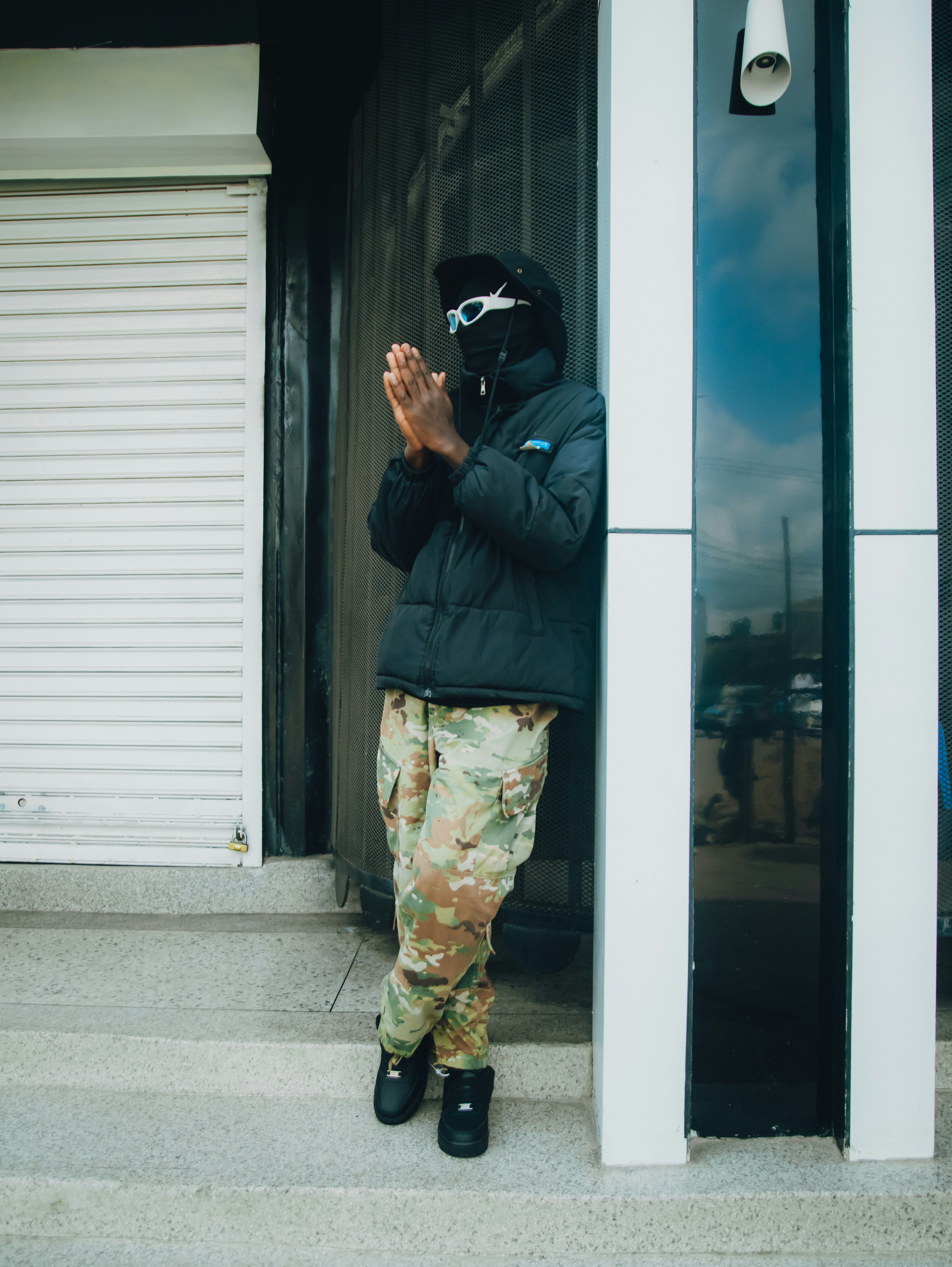 Masked figure in urban doorway claps against a cool urban backdrop